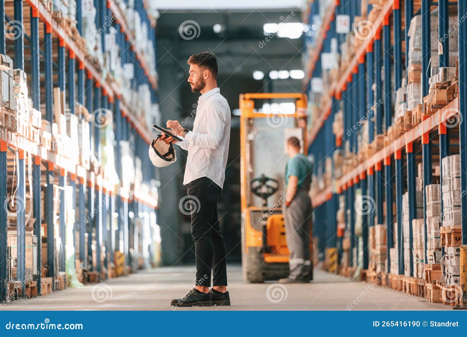 With Tablet in Hands. Storage Worker is in the Warehouse with Bunch of ...