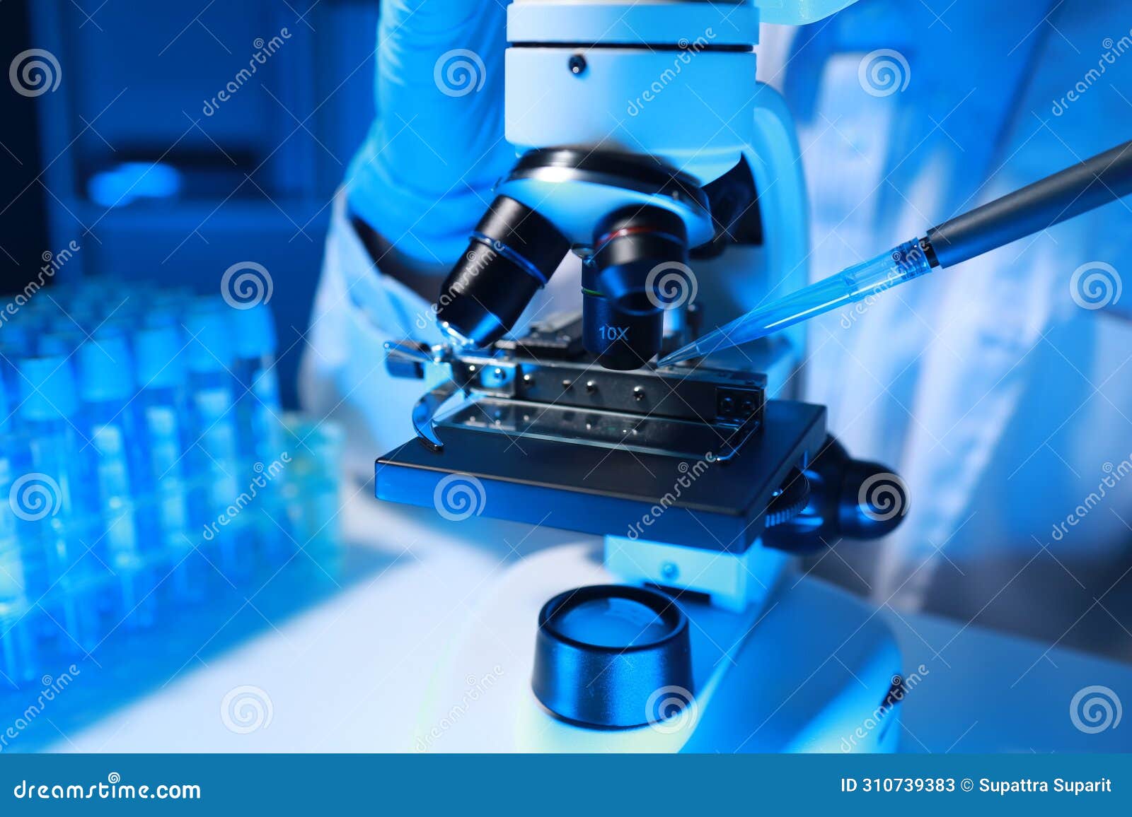 A Talented Scientist Sits in His Lab while Using a Microscope To Look ...