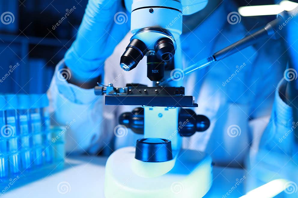 A Talented Scientist Sits in His Lab while Using a Microscope To Look ...