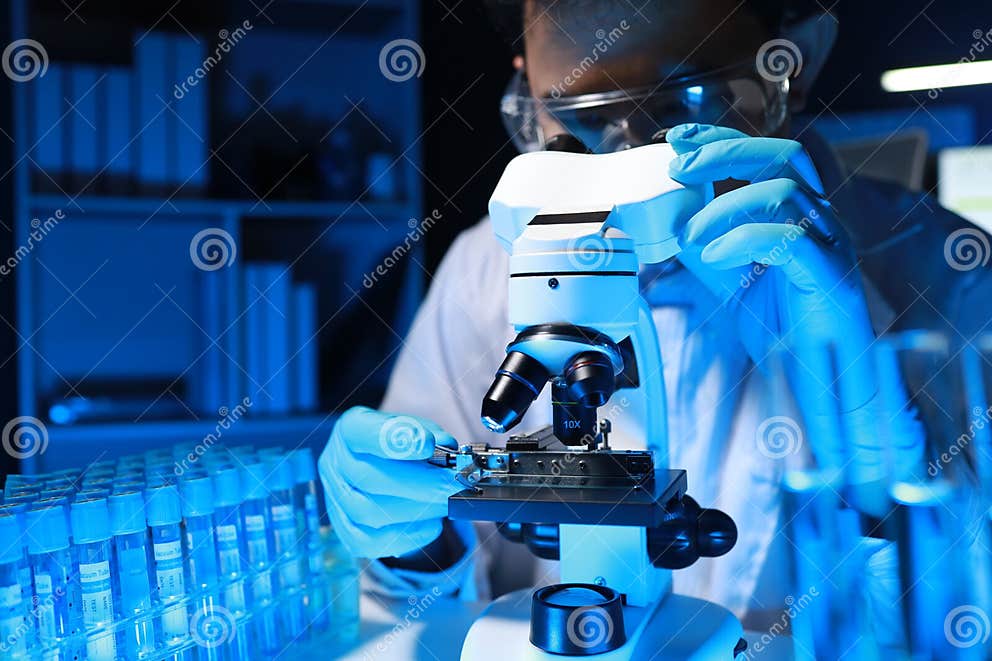 A Talented Scientist Sits in His Lab while Using a Microscope To Look ...