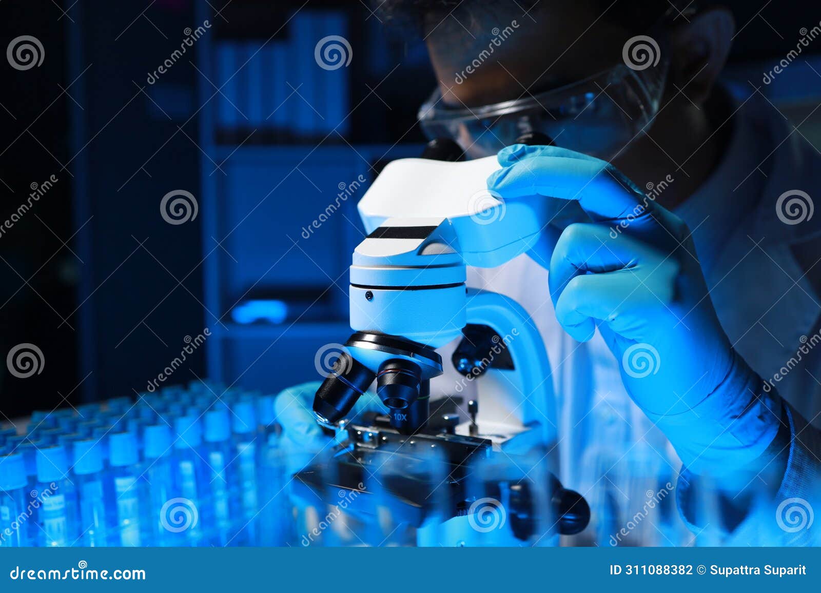 A Talented Scientist Sits in His Lab while Using a Microscope To Look ...