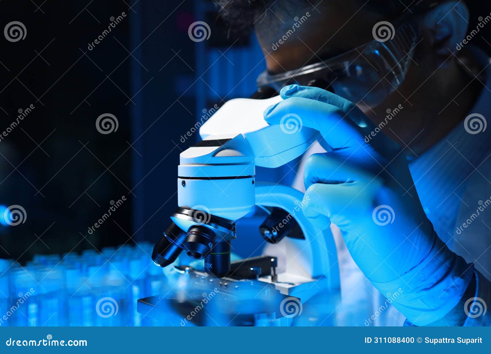 A Talented Scientist Sits in His Lab while Using a Microscope To Look ...