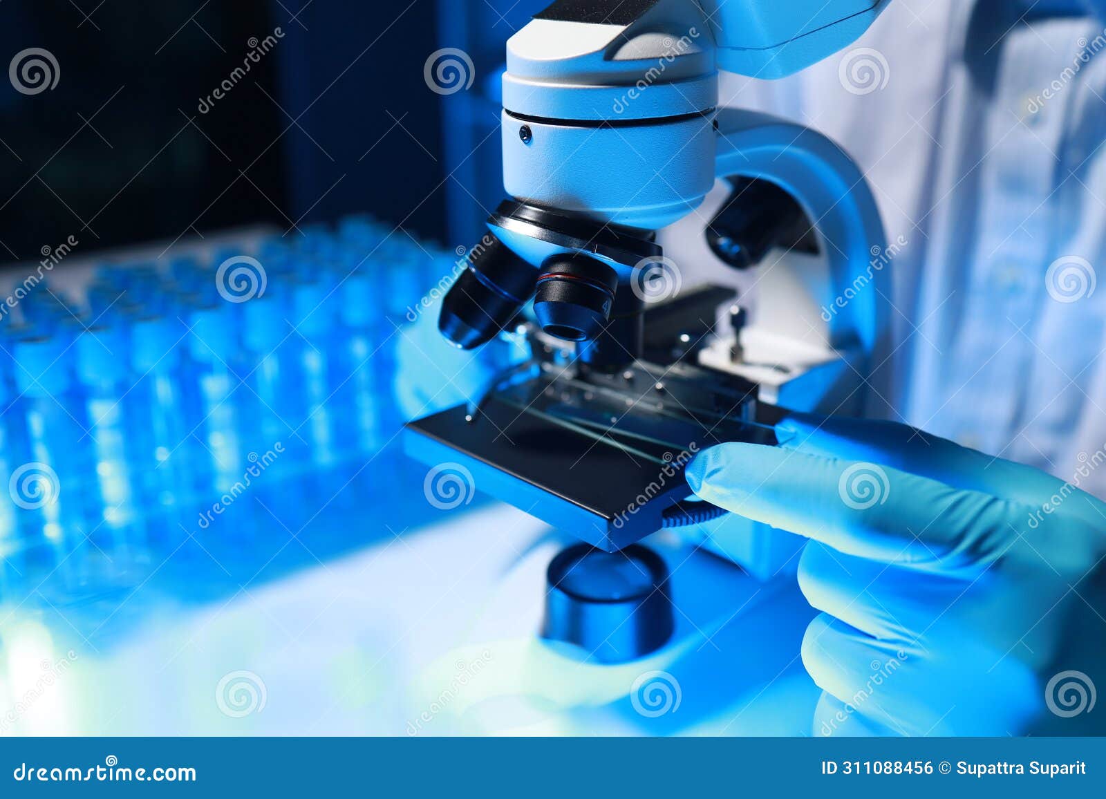 A Talented Scientist Sits in His Lab while Using a Microscope To Look ...