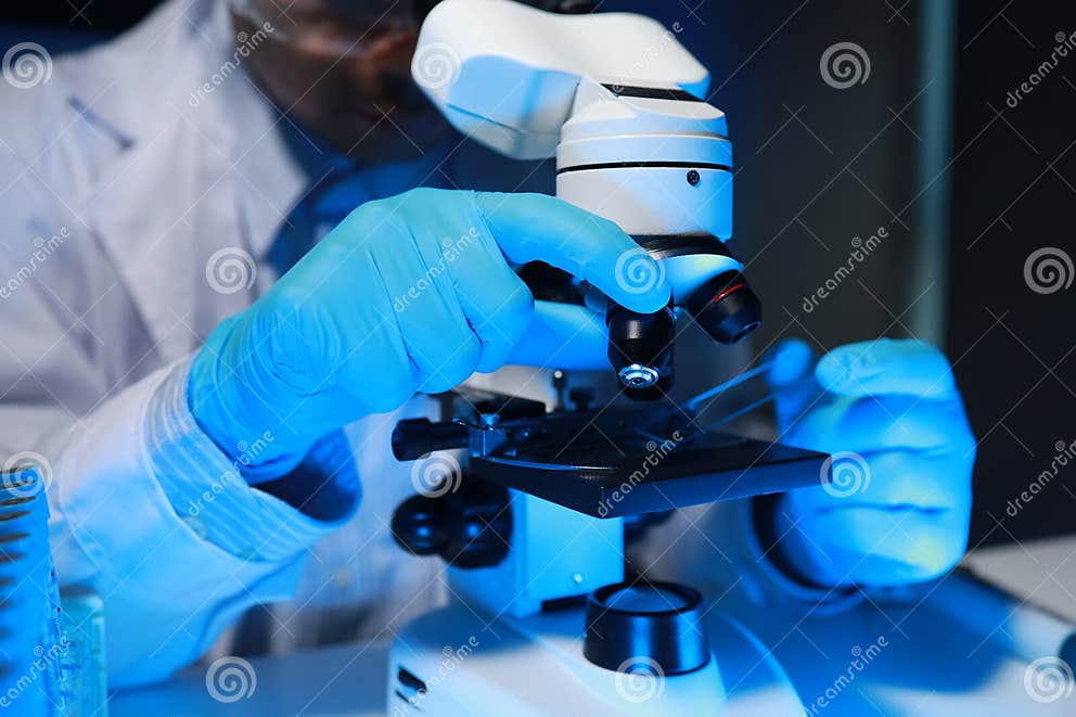 A Talented Scientist Sits in His Lab while Using a Microscope To Look ...