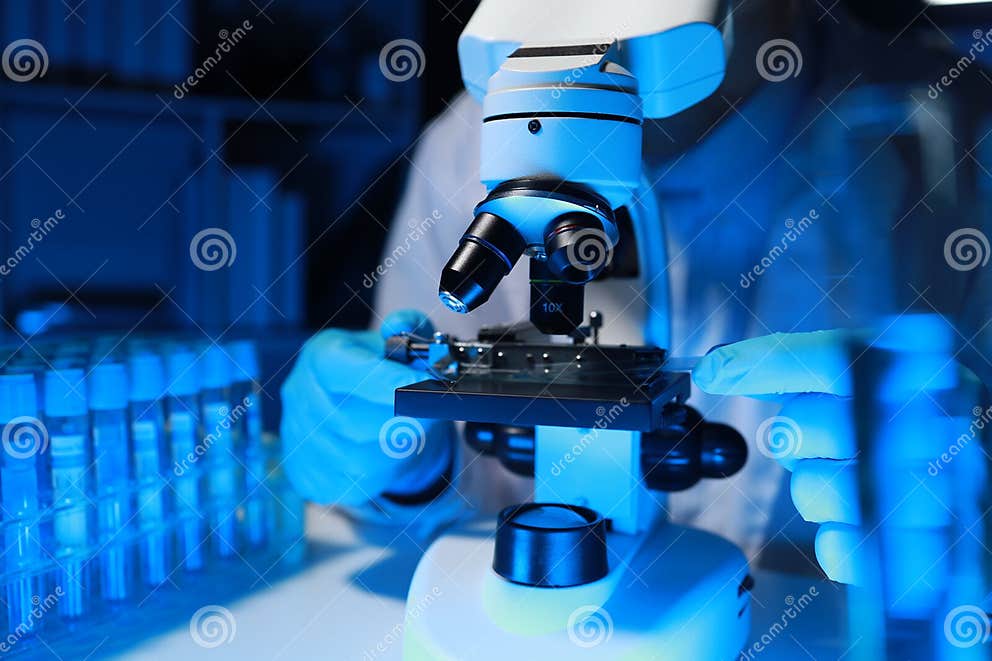 A Talented Scientist Sits in His Lab while Using a Microscope To Look ...