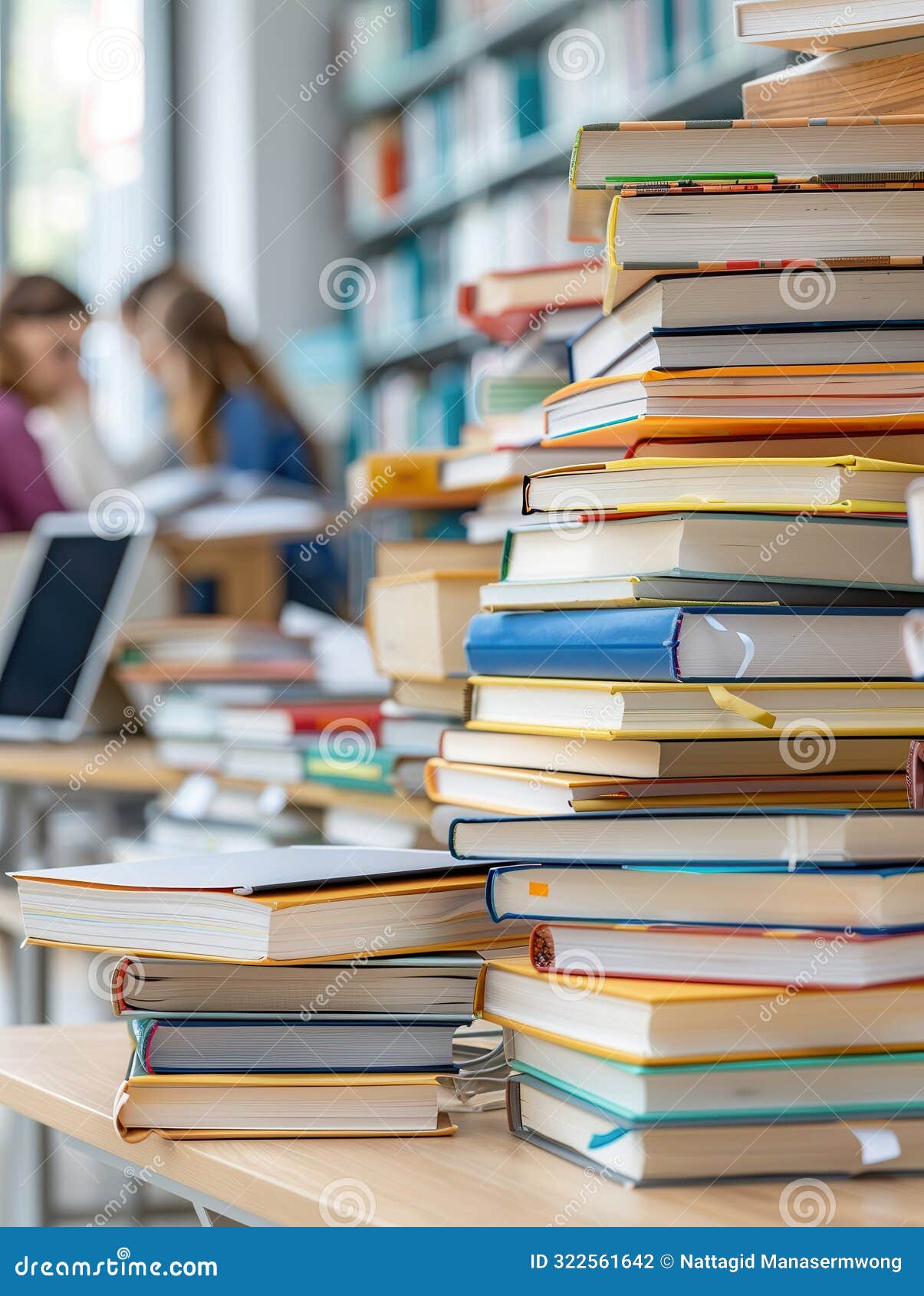 A Tall Stack Of Books On A Table In A Library With Blurred Individuals ...