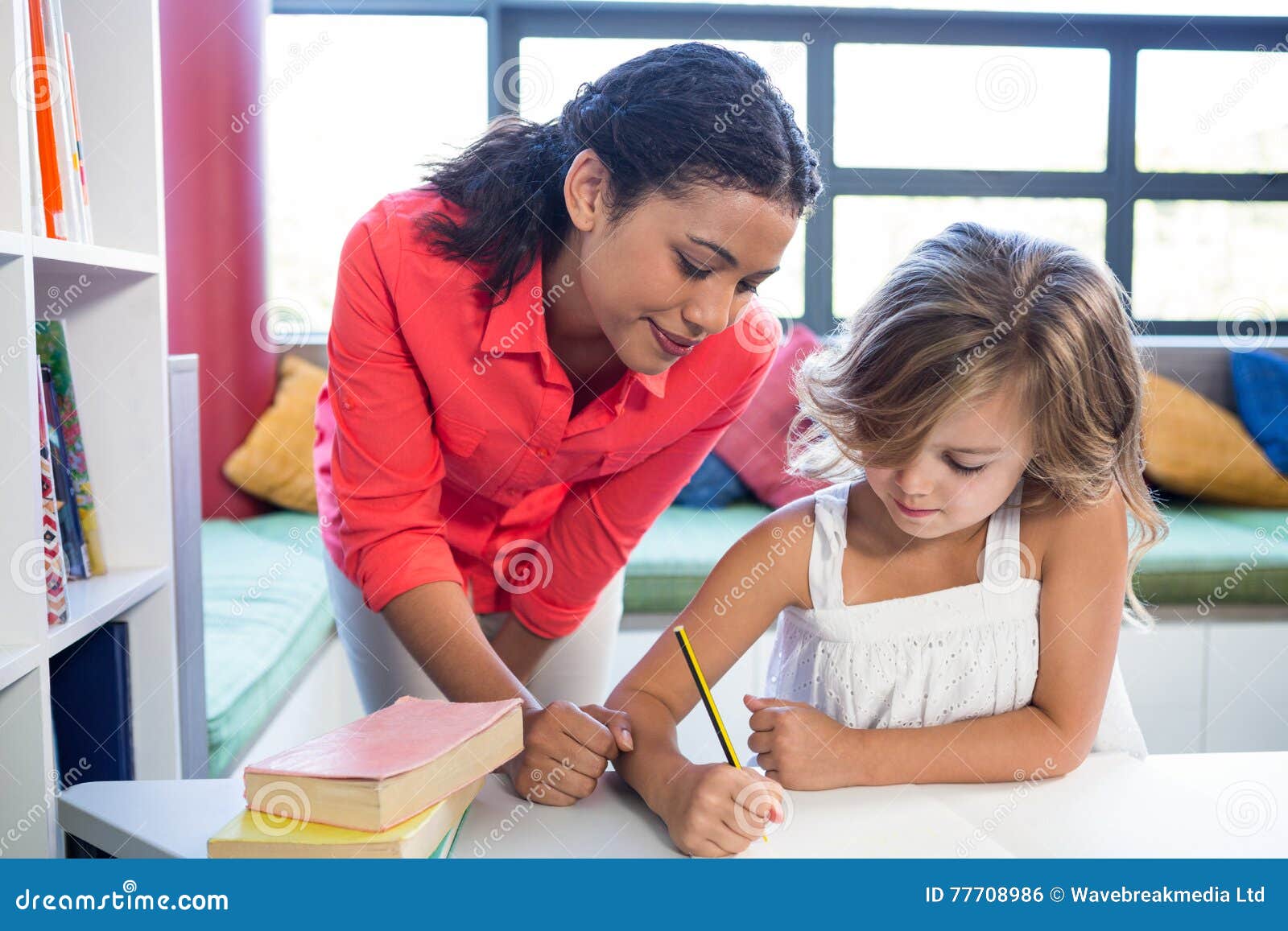 Teacher Assisting Girl Writing on Notebook in Library Stock Photo ...