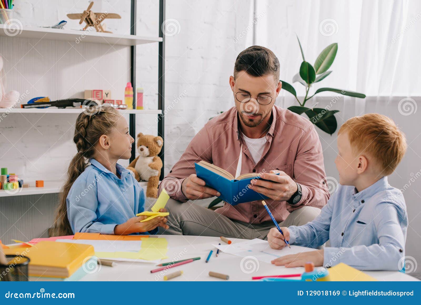 Teacher in Eyeglasses Reading Book To Kids at Table Stock Image - Image ...
