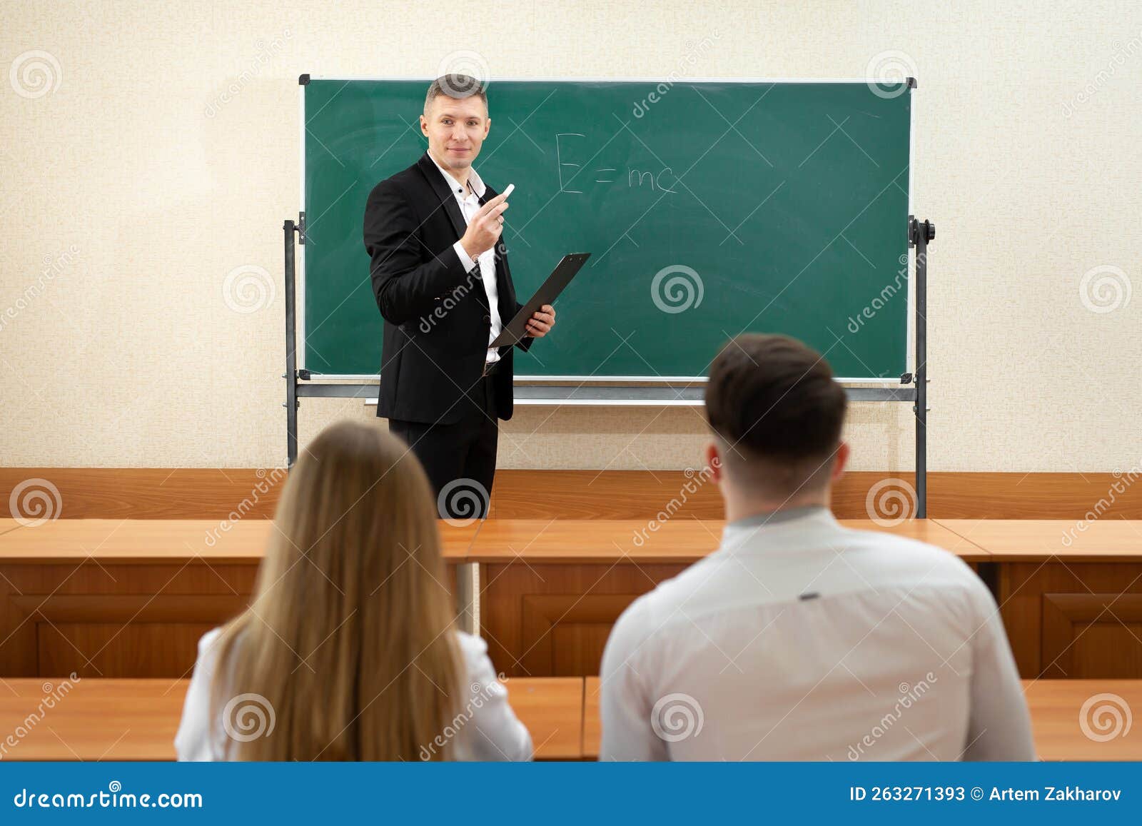 Teacher Giving a Lecture in a Classroom and Writing Math Formulas on ...