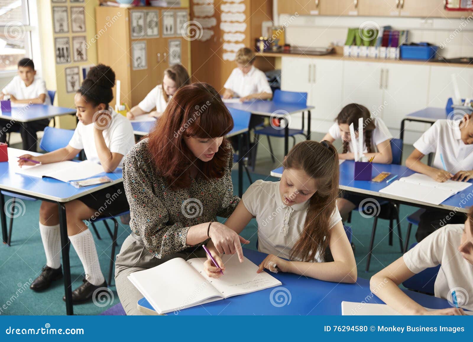 Teacher Helping a Girl with Work at Her Desk, Elevated View Stock Photo ...