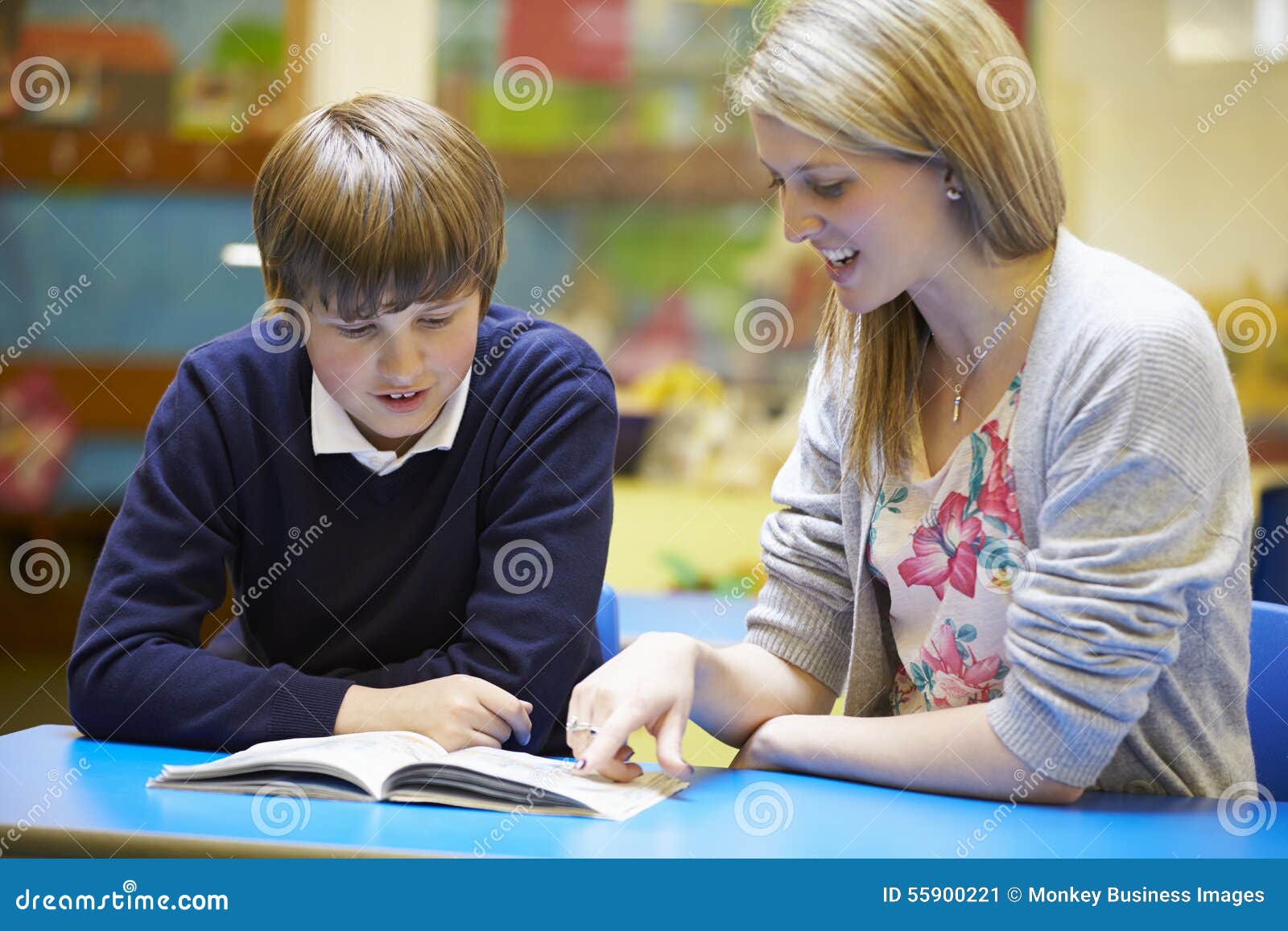 Teacher with Male Pupil Reading at Desk in Classroom Stock Image ...
