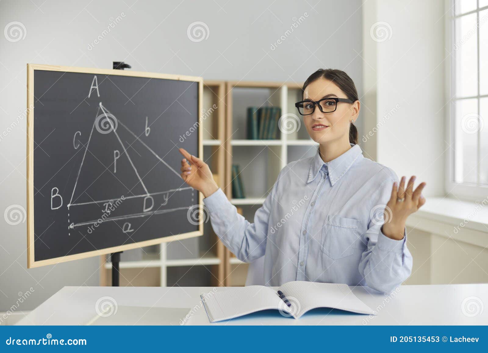 Teacher Sitting Desk, Pointing at Board and Teaching Students How To ...