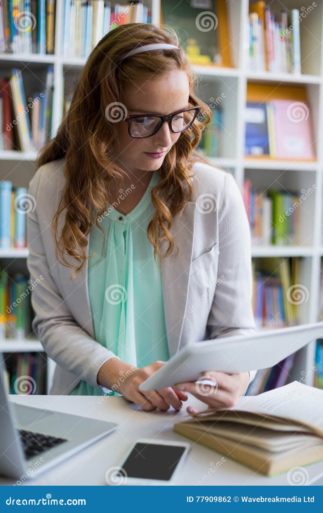 Teacher Using Digital Tablet with Laptop and Phone on Table in Library ...