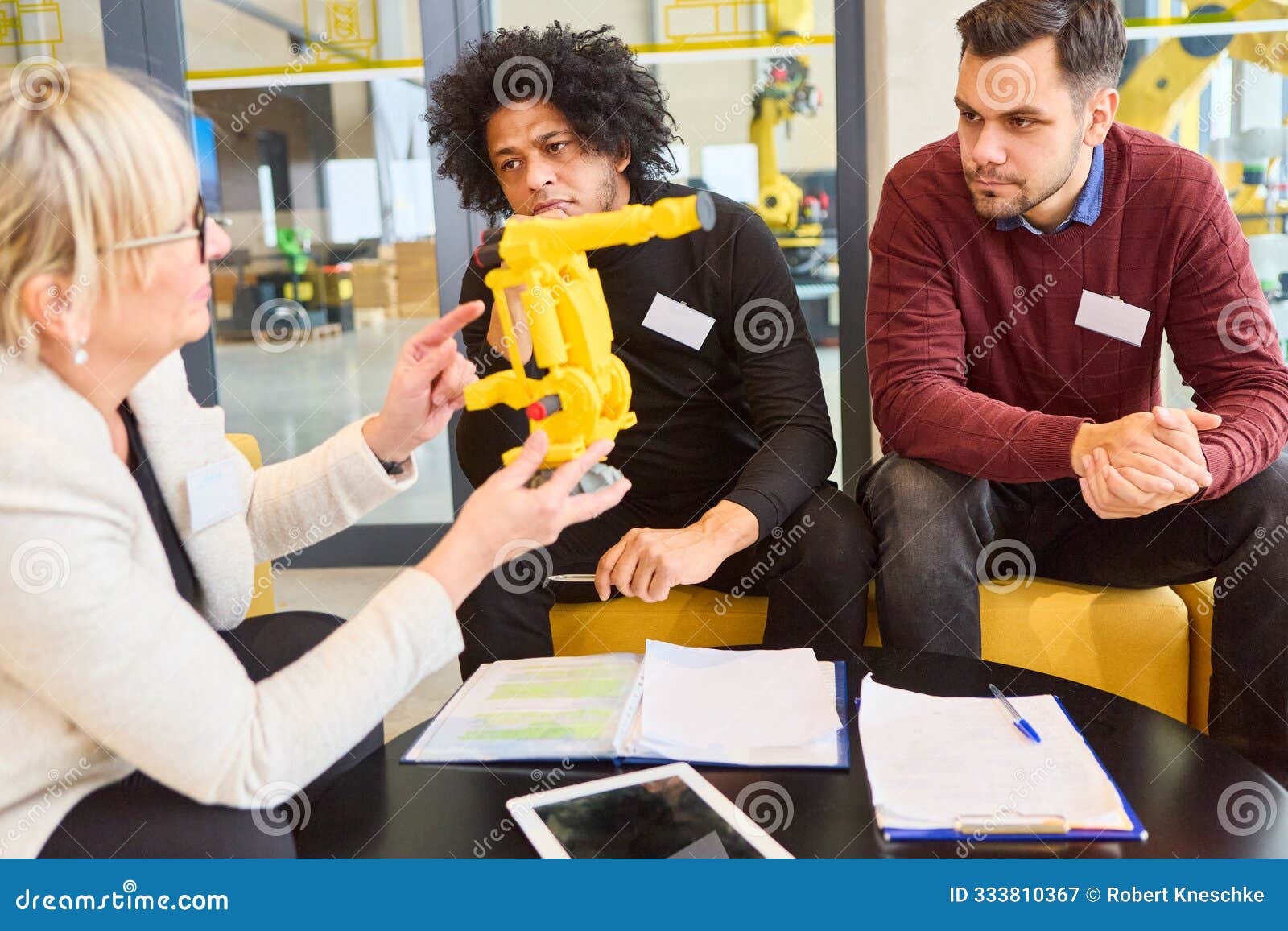 Team Discussing Robotics Development and Automation with a Gripper Arm Model in Office Setting ...