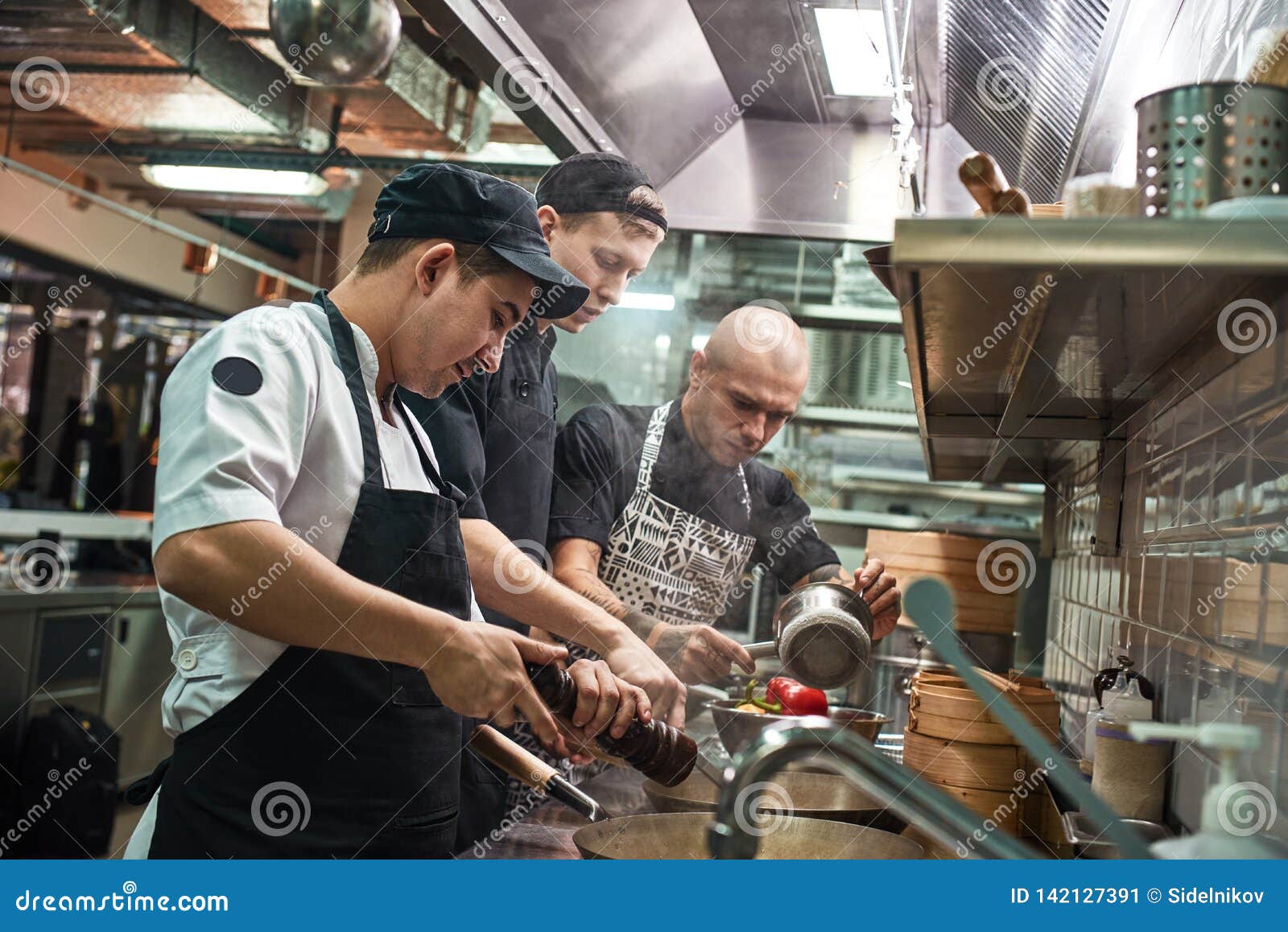 Teamwork. Restaurant Chef and His Two Assistants in Aprons Cooking a ...