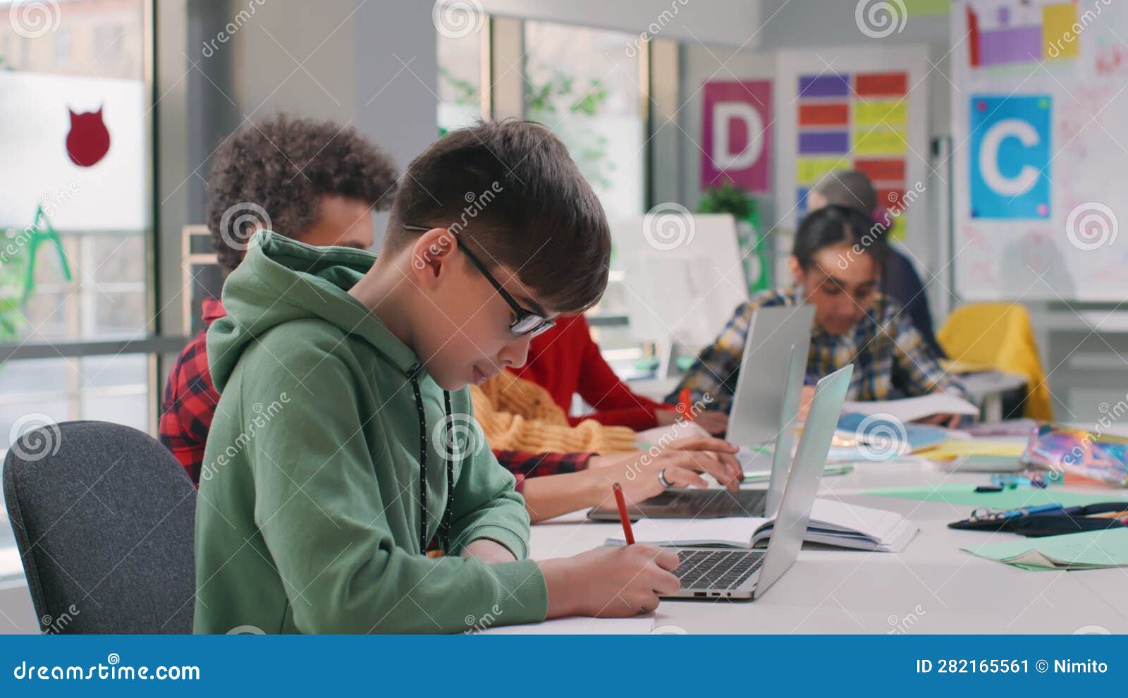 Teenage Male Student Sit Down at Desk and Write Task in Notebook Using ...