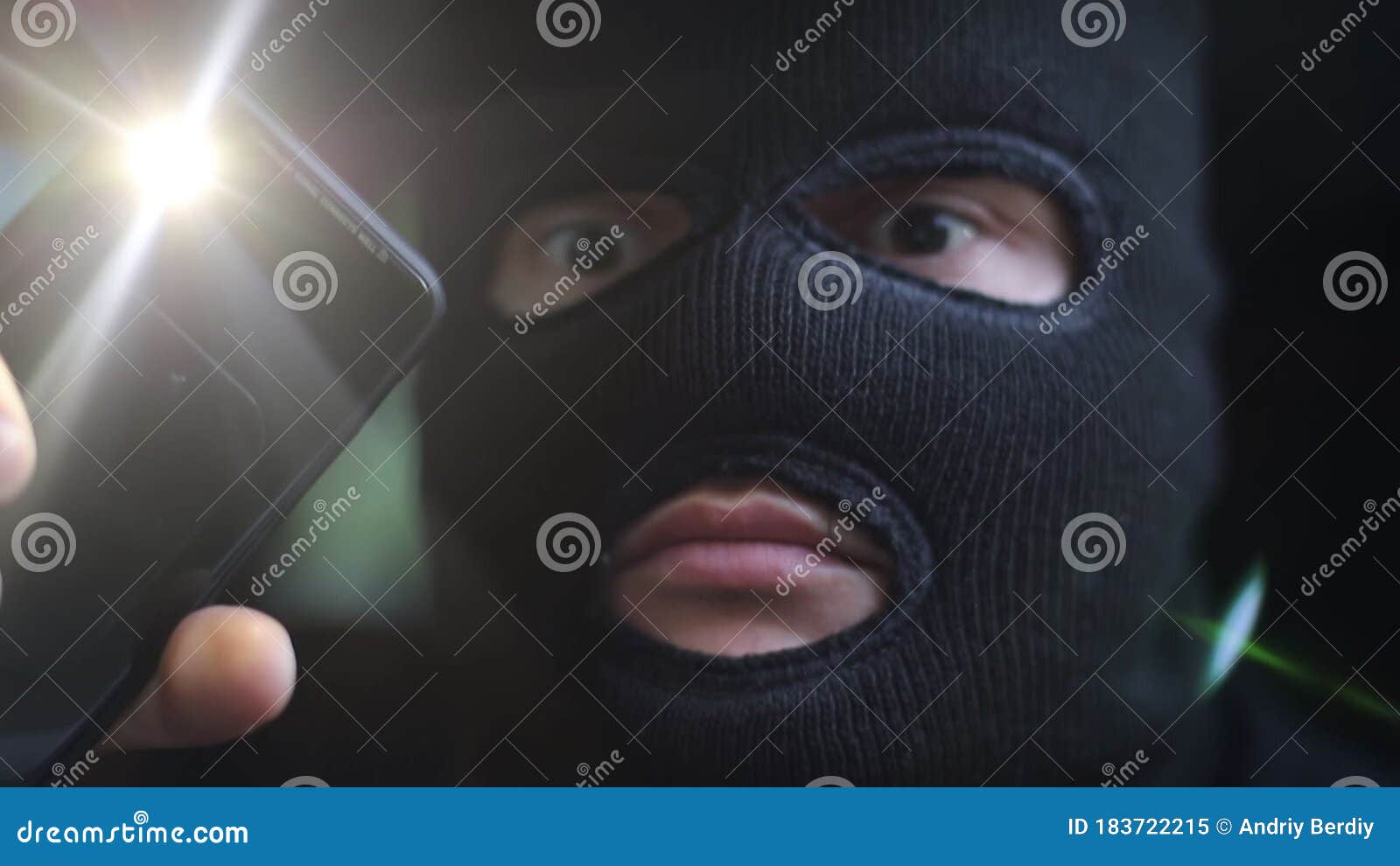 A Terrorist with a Flashlight in a Dark Mask Looks into the Camera ...