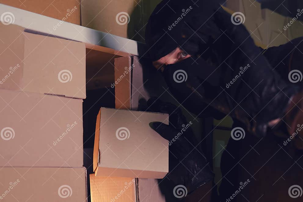A Thief Takes a Box with a Parcel in a Warehouse at Night. Concept of ...
