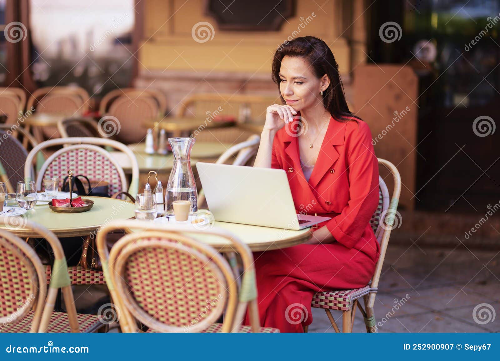 Thinking Woman Sitting At Outdoor Cafe And Using Her Laptop Stock Image