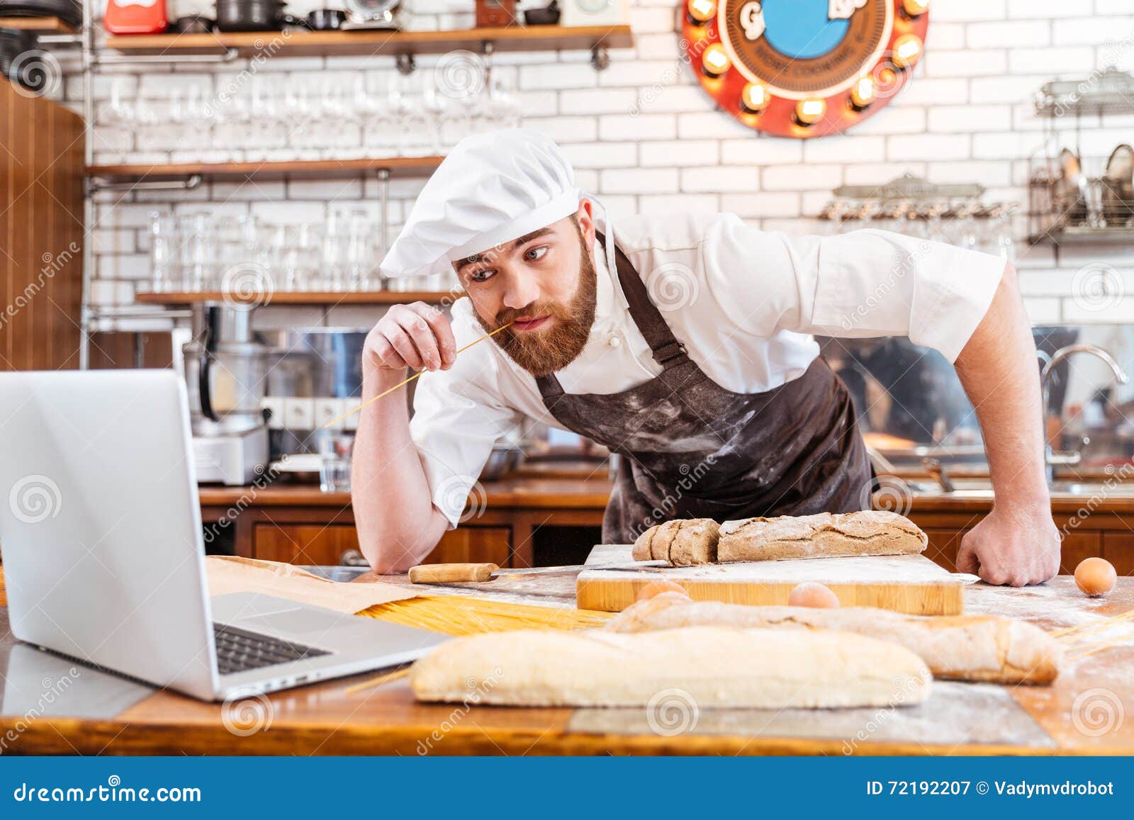 Thoughtful Baker Cutting Bread and Using Laptop on Kitchen Stock Image ...