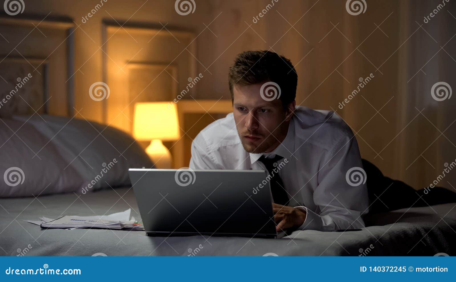 Thoughtful Male Lying on Bed and Reading Documents on Laptop, Business ...