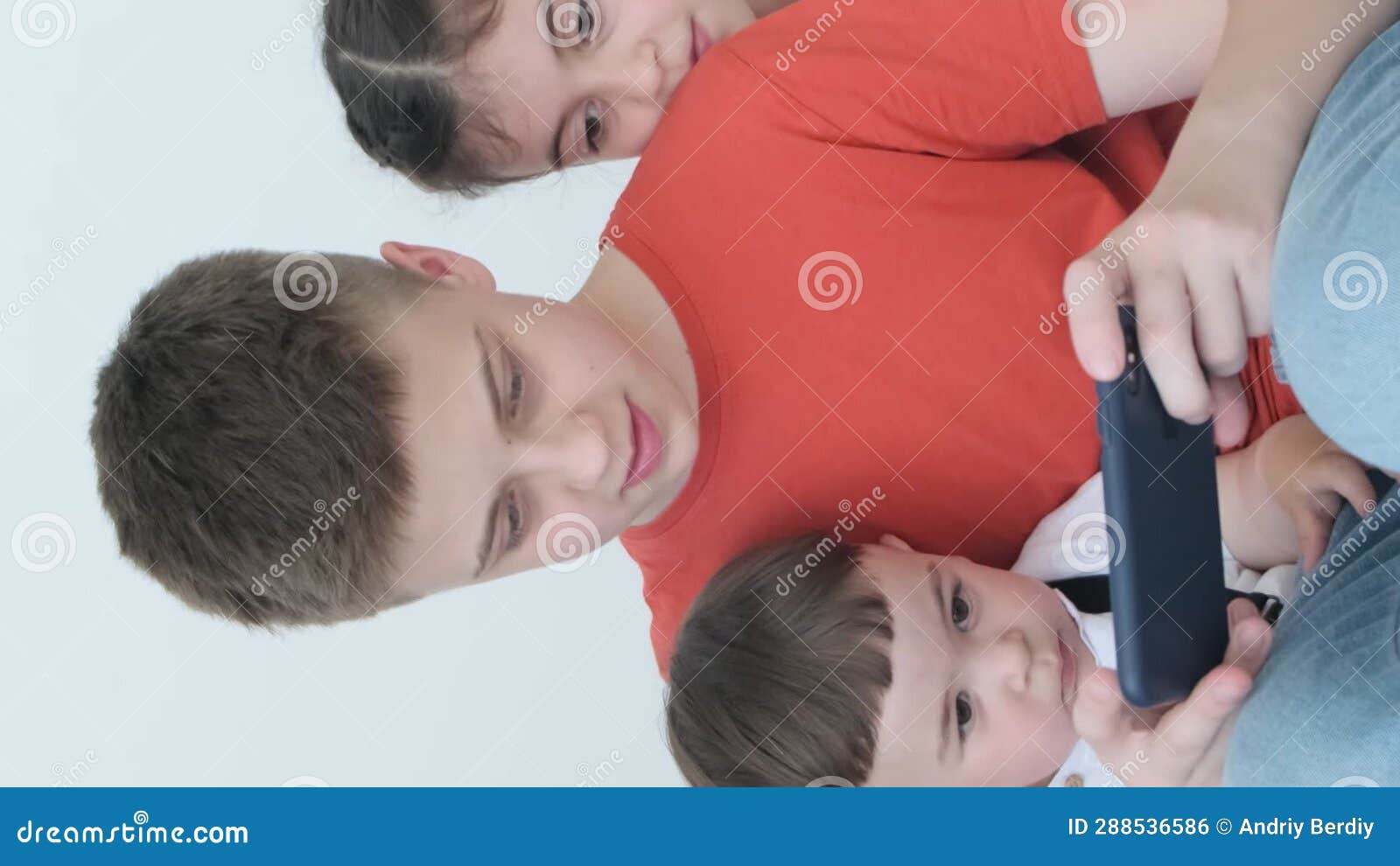 Three Children of Different Ages are Using a Smartphone while Sitting ...