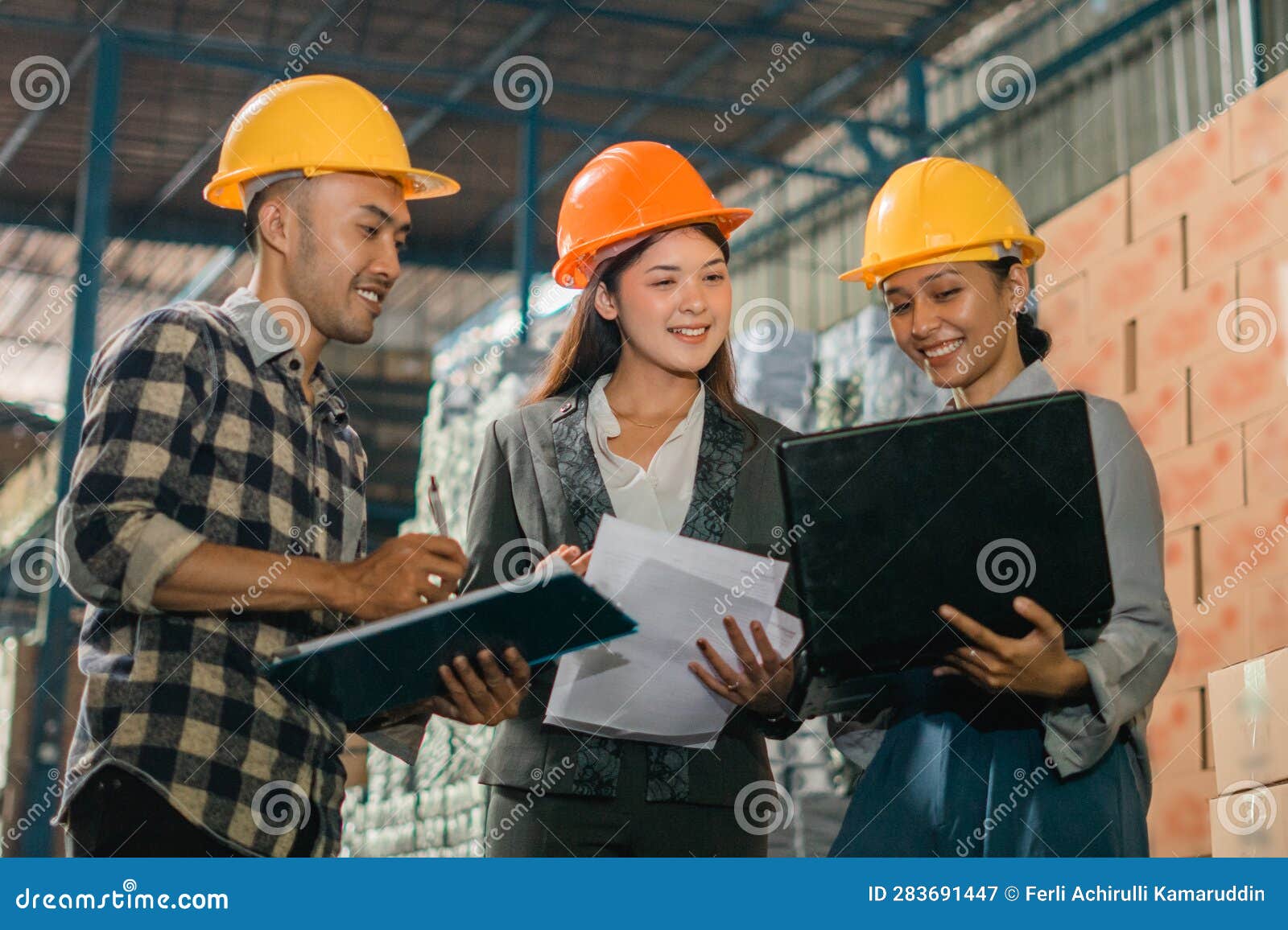 Three Factory Employees Stand at Work Matching Data and Using a Laptop ...