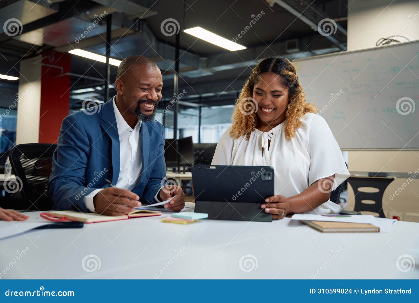 Three Happy Multiracial Colleagues Looking Down and Smiling while Using ...