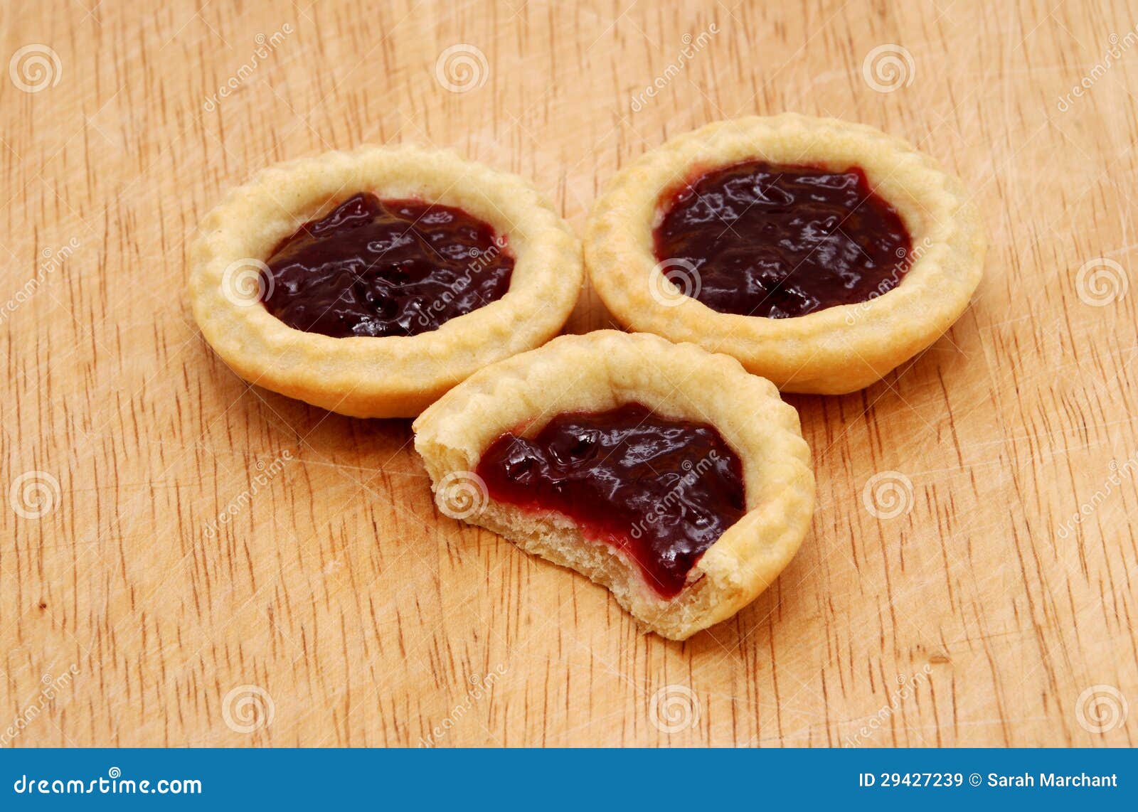 Three Jam Tarts, One with a Bite Taken, on a Wooden Table Stock Image ...