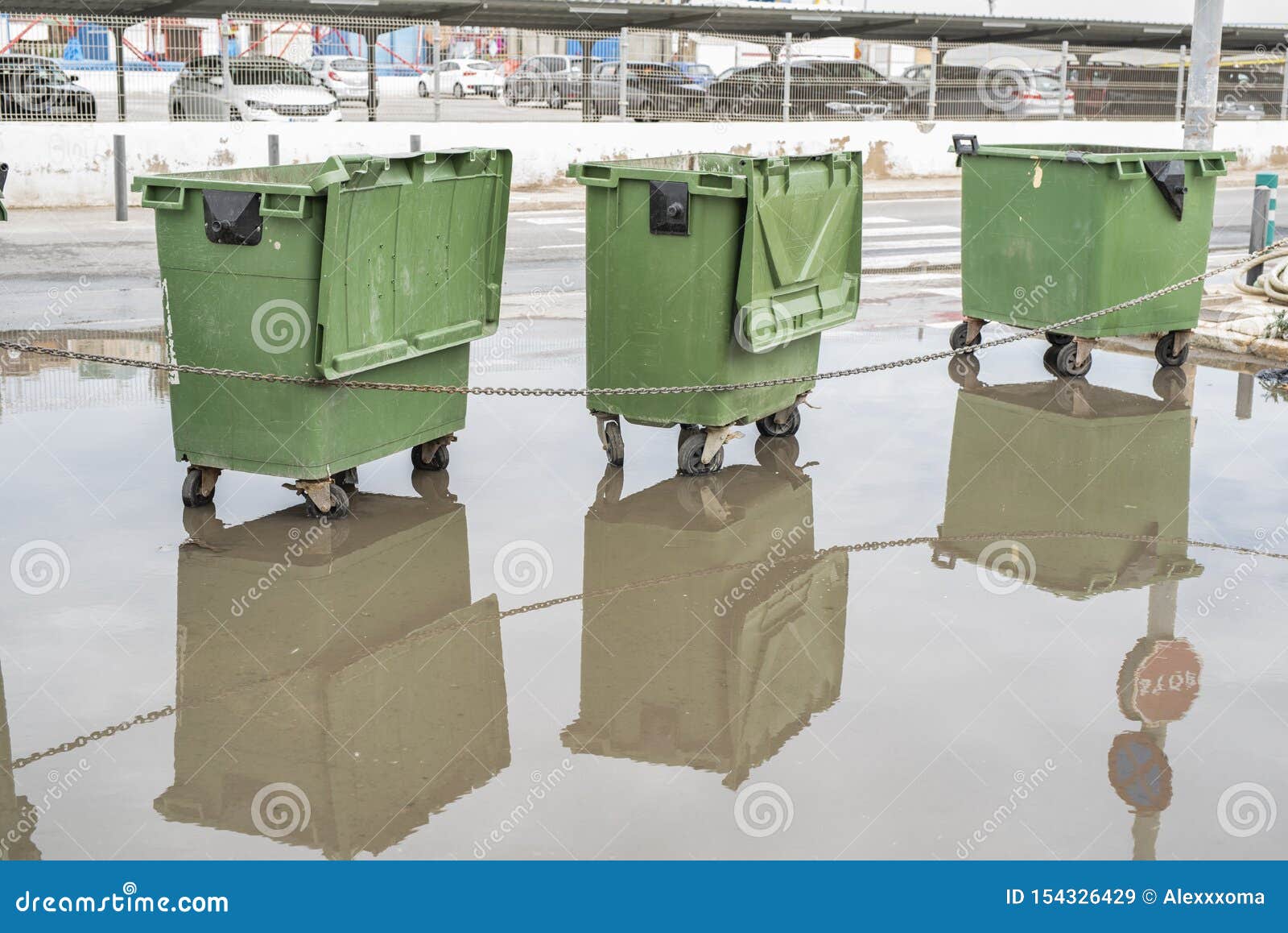 Three Large Green Plastic Waste Bins on Wheels Reflected in Rain Puddle ...