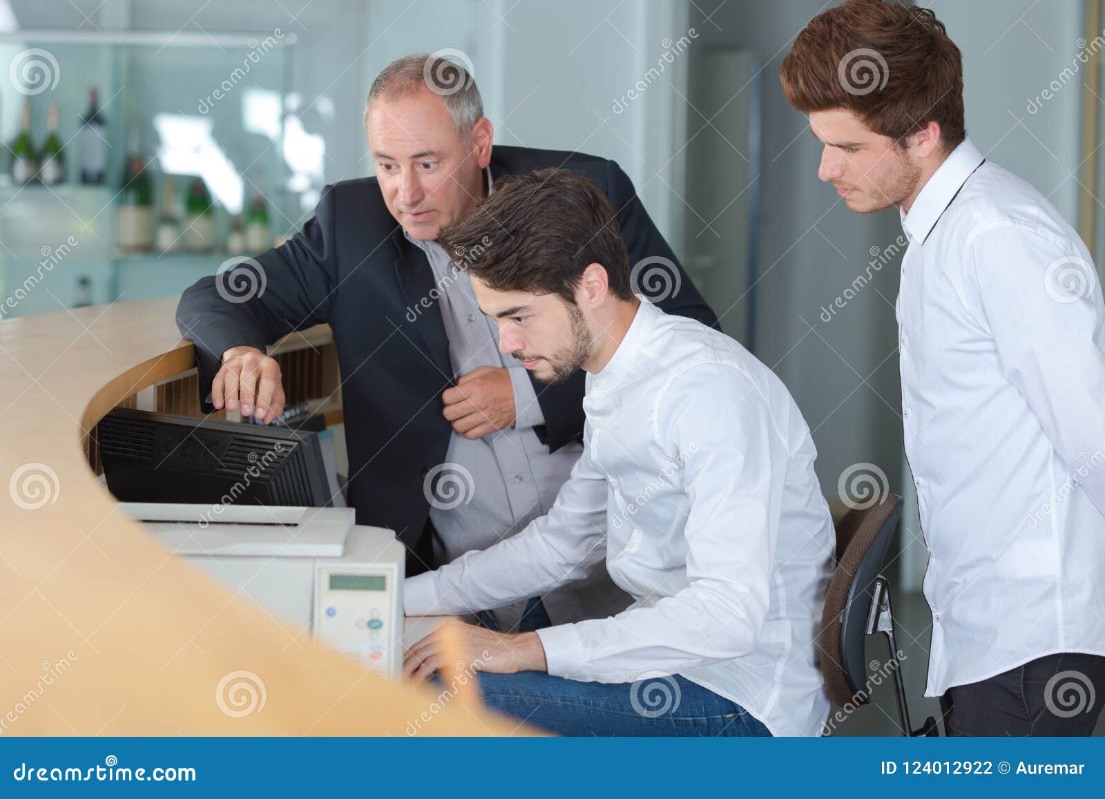Three Men Looking at Computer Behind Reception Desk Stock Photo - Image ...