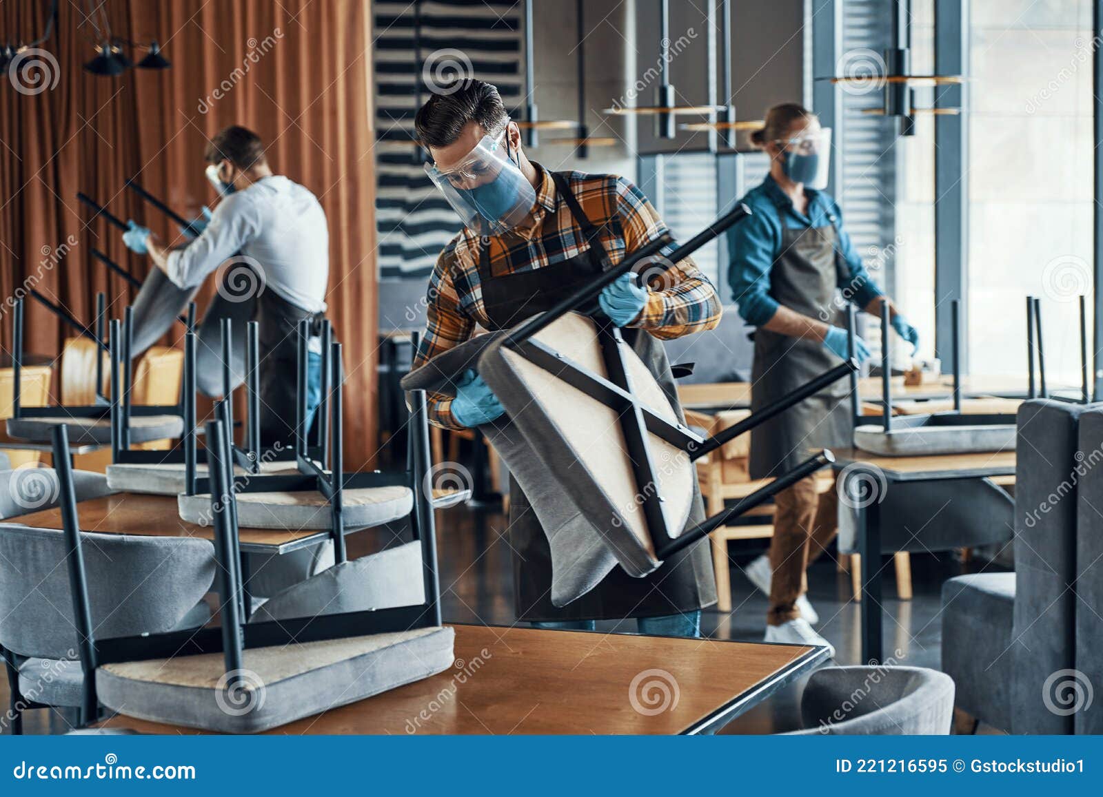 Three Men in Protective Face Shields and Aprons Arranging Furniture in ...