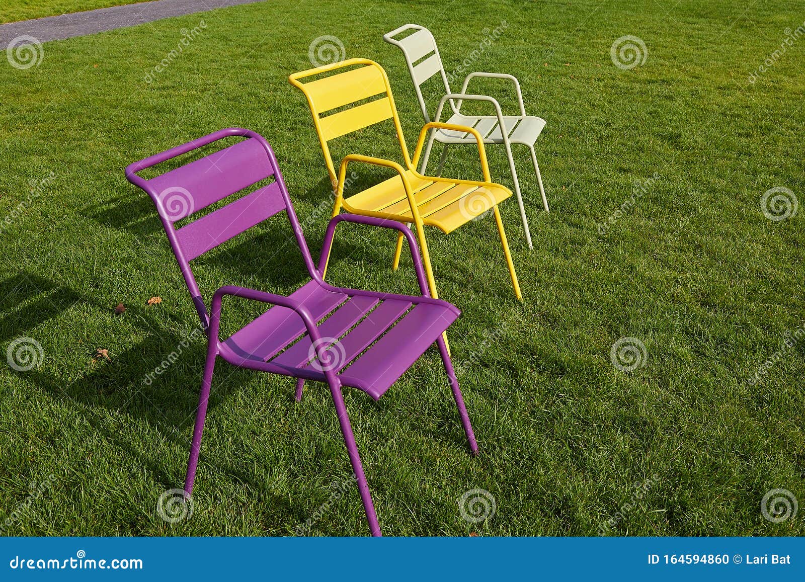 Three Multi-colored Metal Chairs Stand on a Green Lawn in the Rays of ...