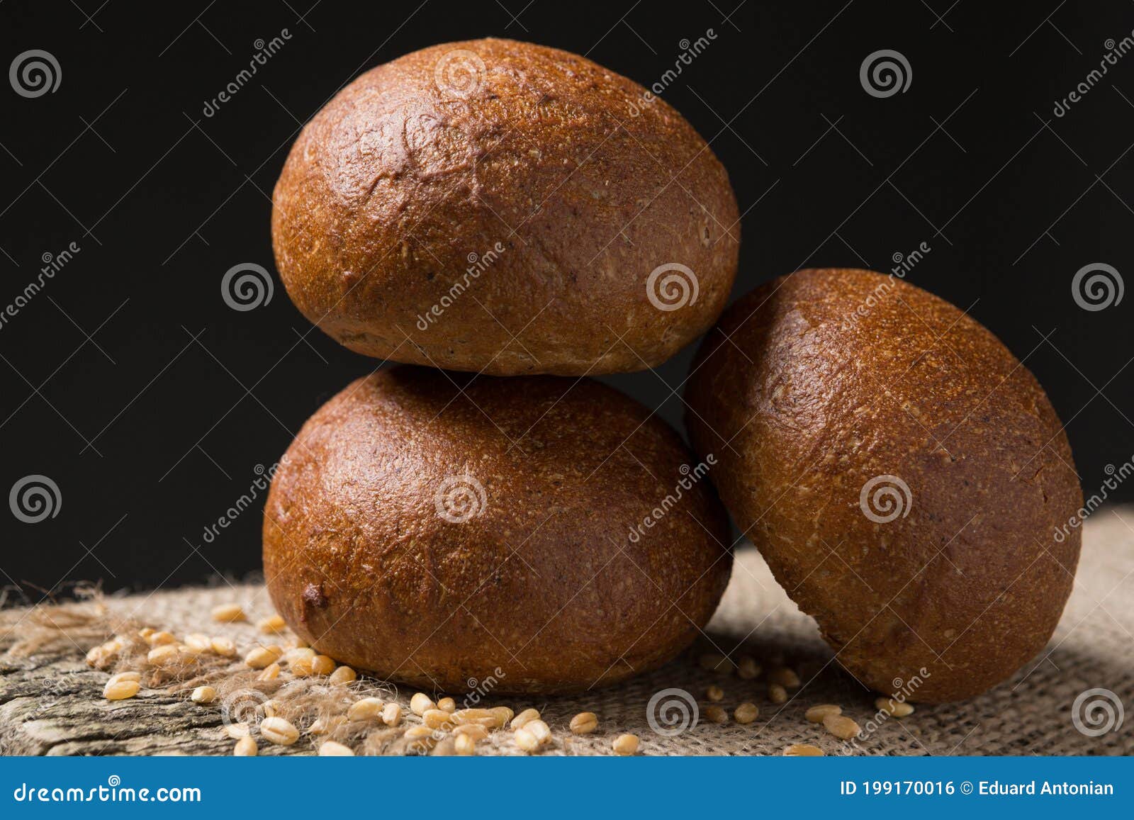 Three Rolls of Dark Bread on a Wooden Board with Wheat Grains, Black ...