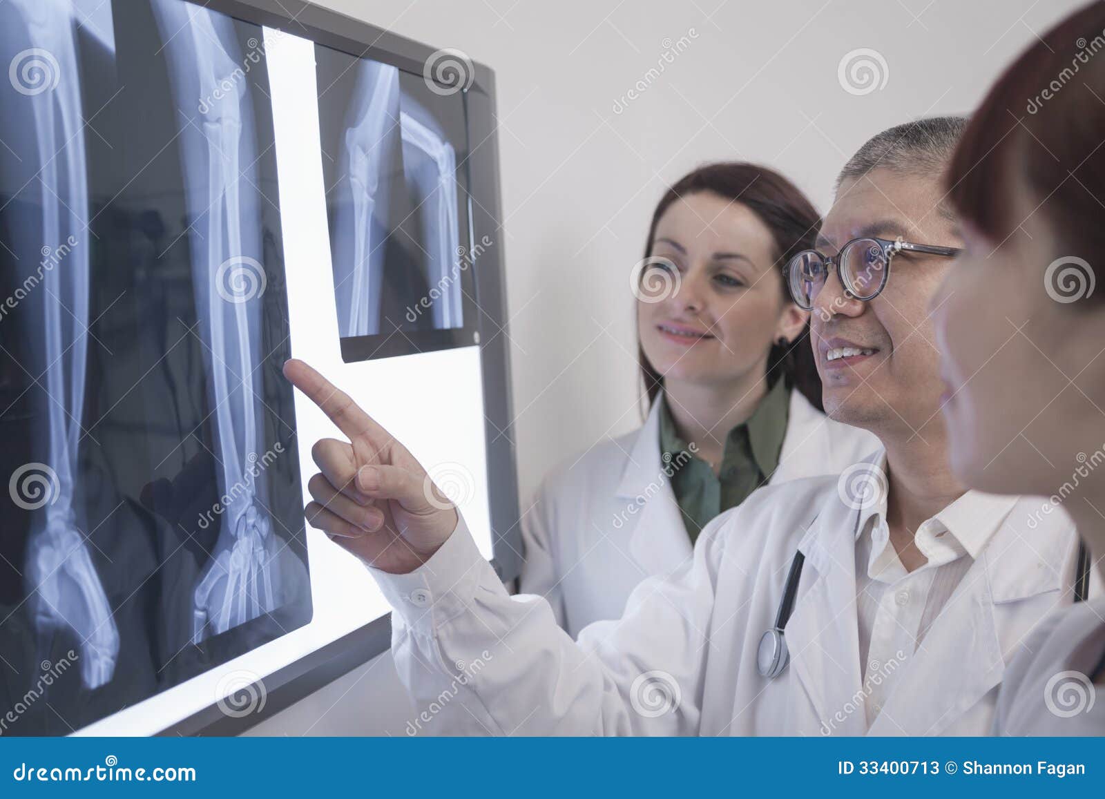 Three Smiling Doctors Looking at X-rays of Human Bones, One Doctor is ...