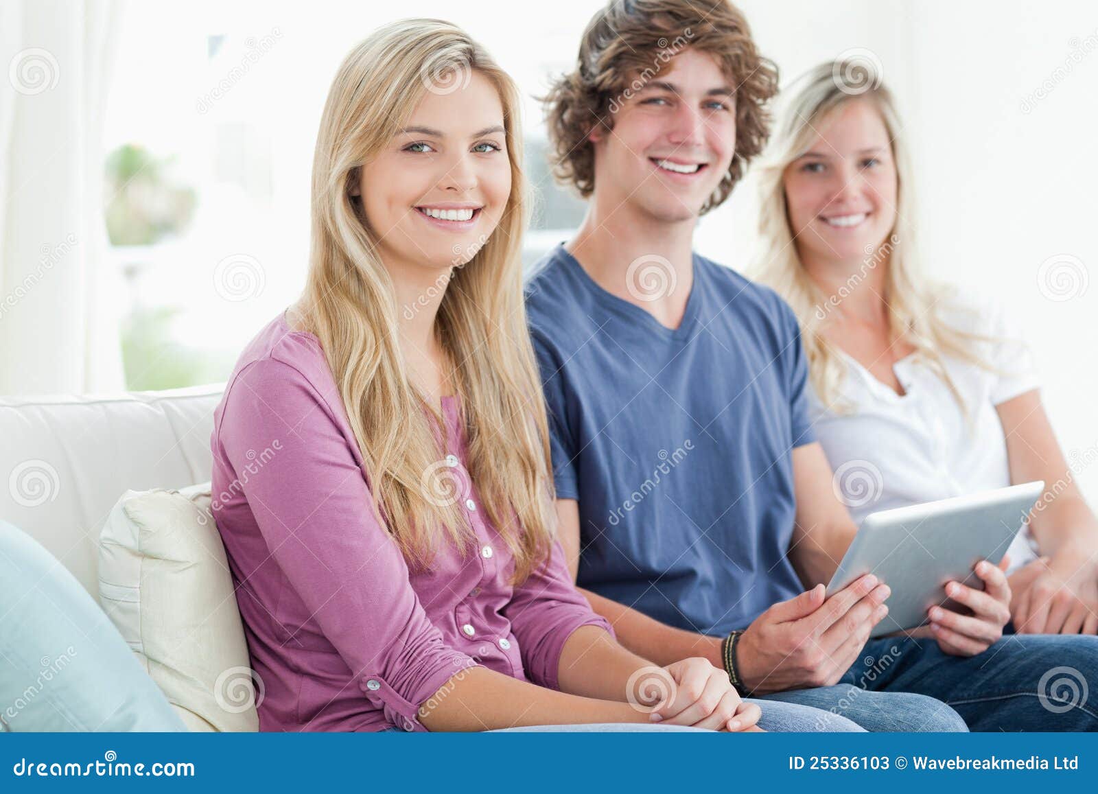 Three Smiling People Sit Together on the Couch with a Tablet Stock ...