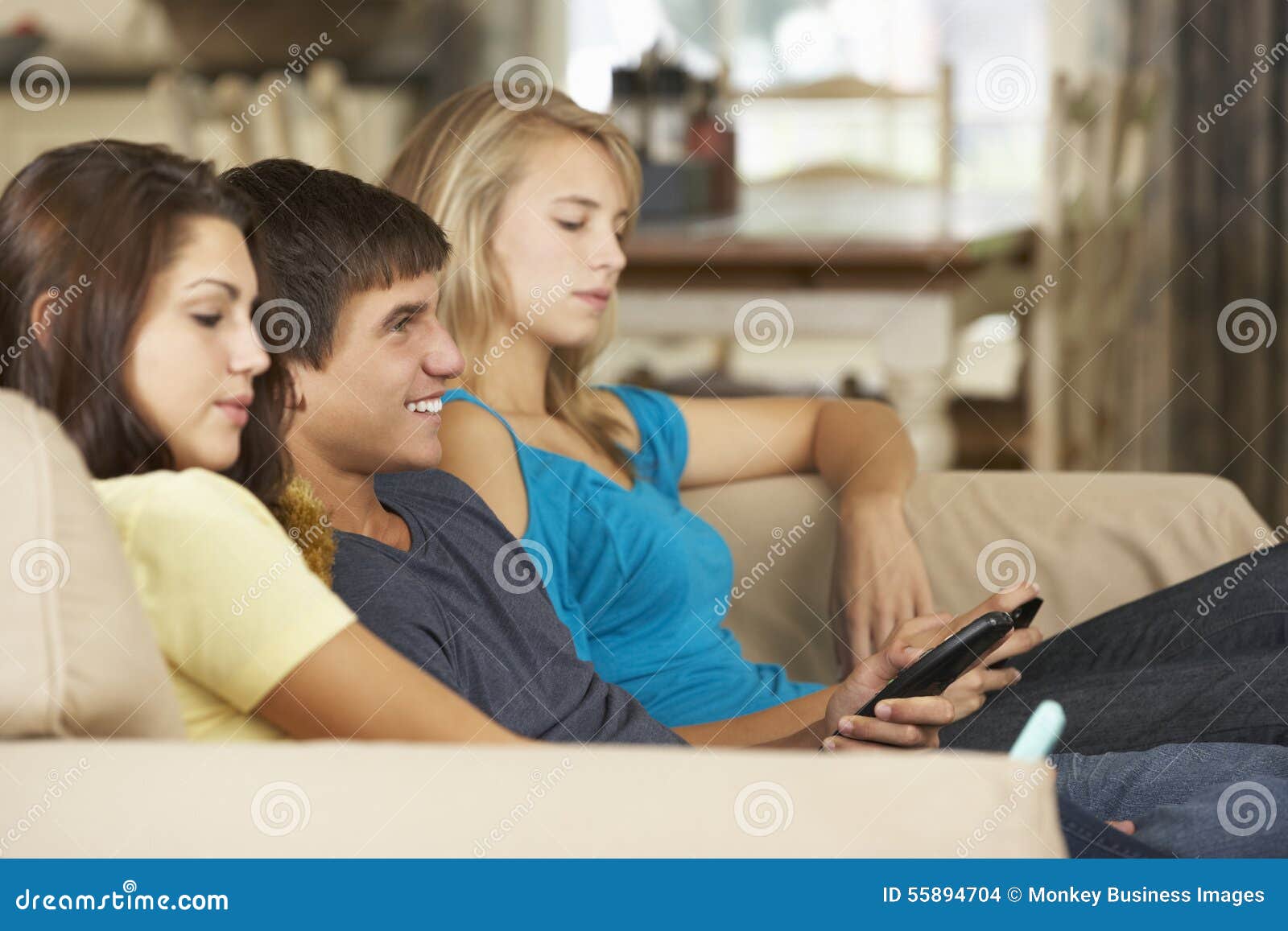 Three Teenagers Sitting on Sofa at Home Texting on Mobile Phones Stock ...