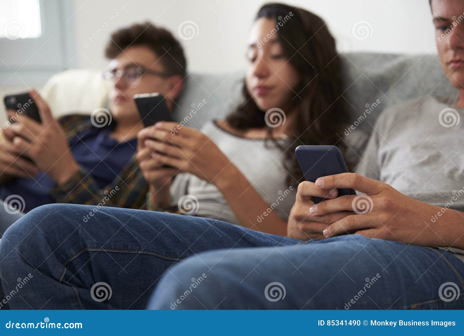 Three Teenagers Sitting Together Using Smartphones at Home Stock Photo ...