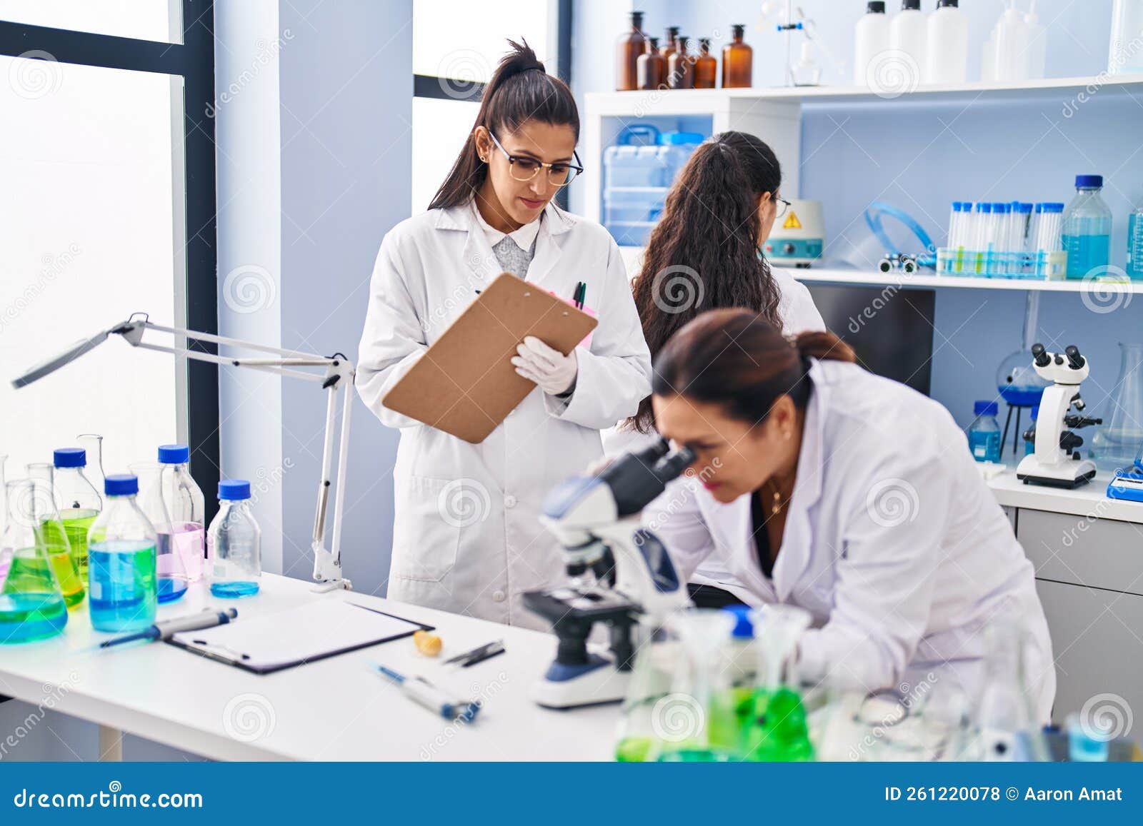 Three Woman Scientists Using Microscope Write on Checklist at ...
