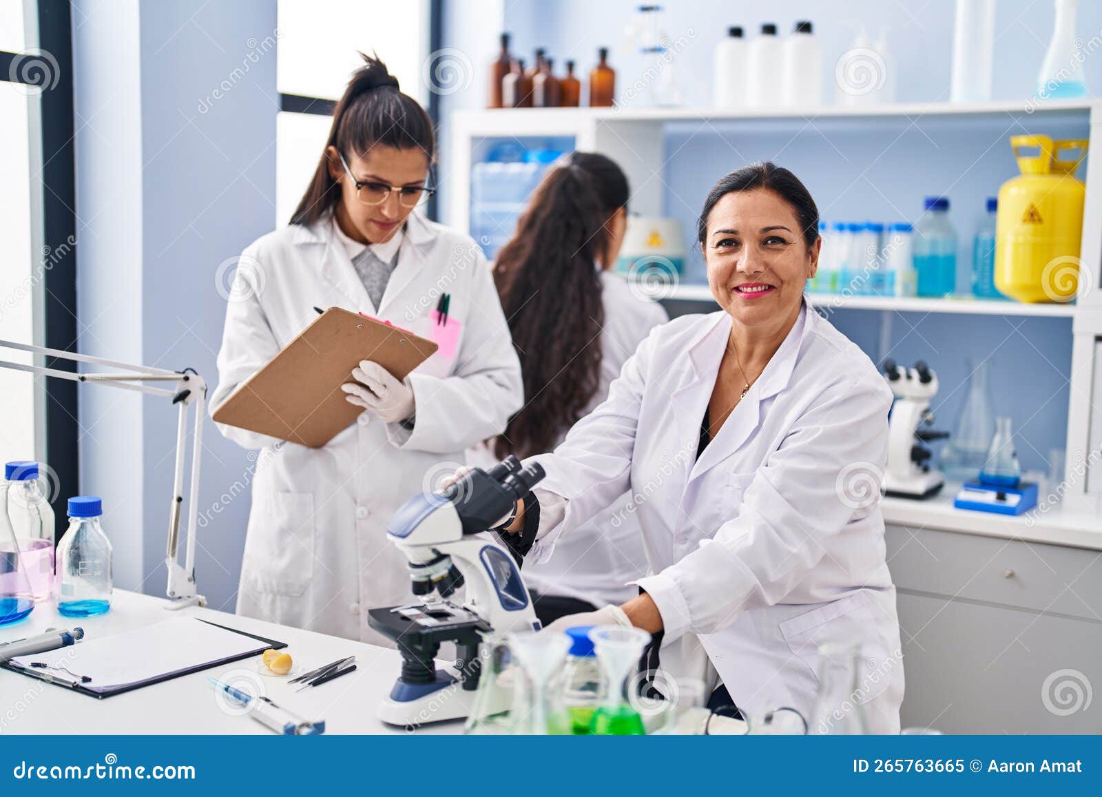 Three Woman Scientists Using Microscope Write on Checklist at ...