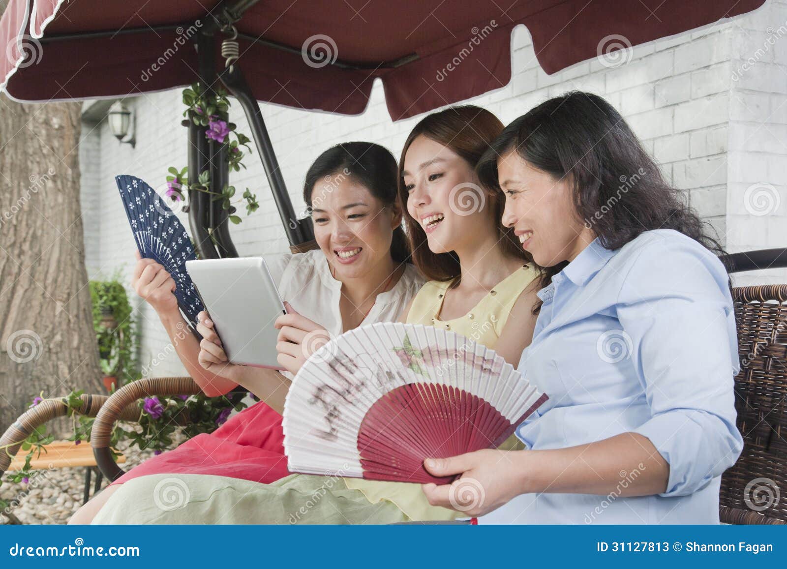 Three Women Smiling and Relaxing with Fans and Tablet Outdoors Stock ...