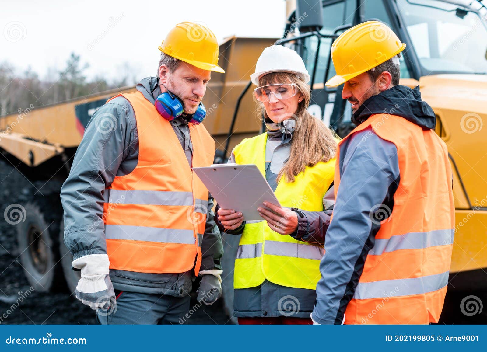 Three Workers in a Quarry Discussing in Front of Heavy Machinery Stock ...