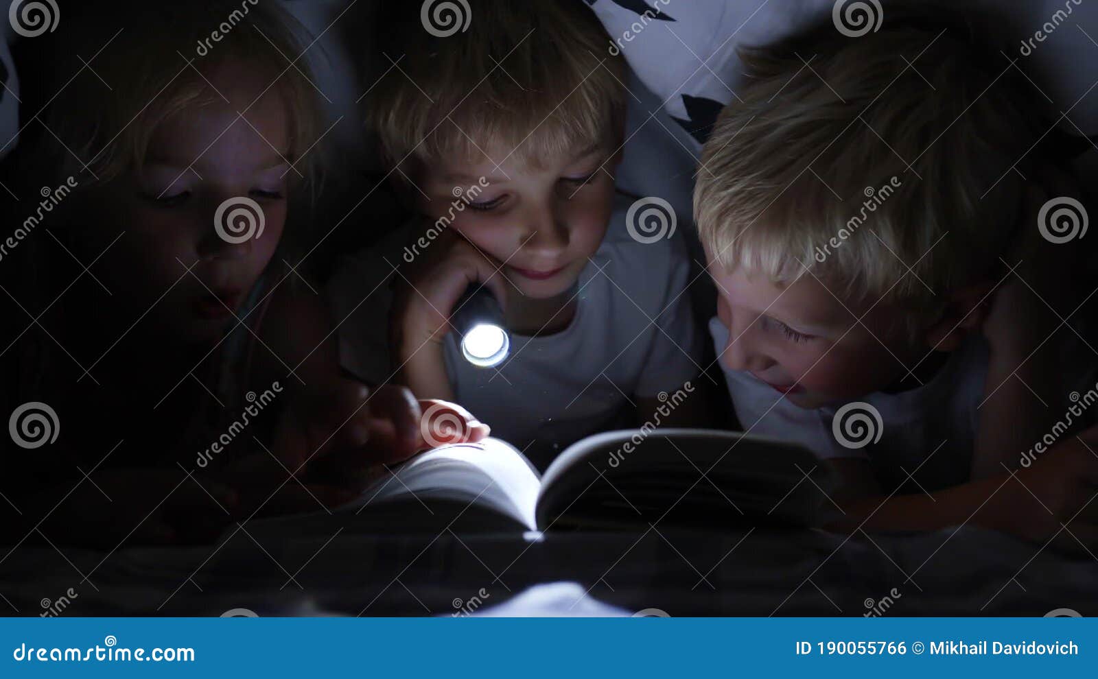 Three Young Children are Reading a Book with a Flashlight Under the ...