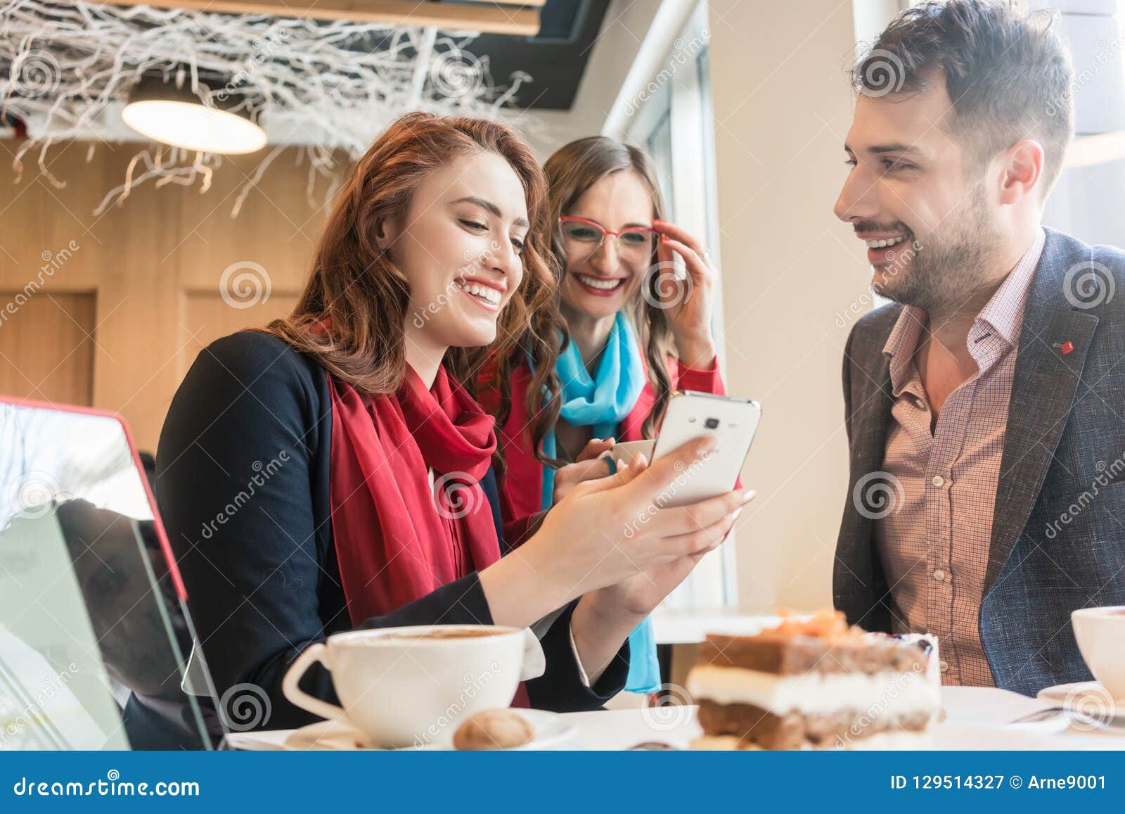 Three Young Friends Using a Mobile Phone for Fun during a Coffee Break ...