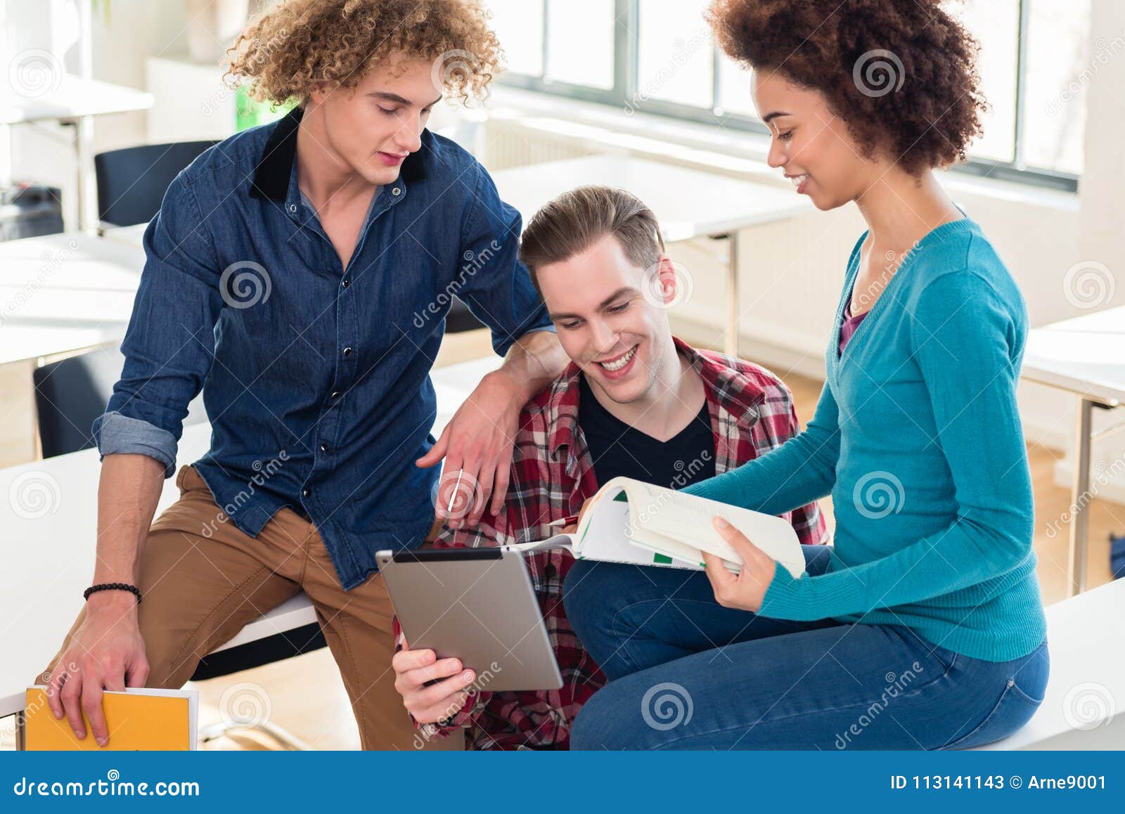 Three Young Students Using Both a Book and a Tablet PC for Checking ...