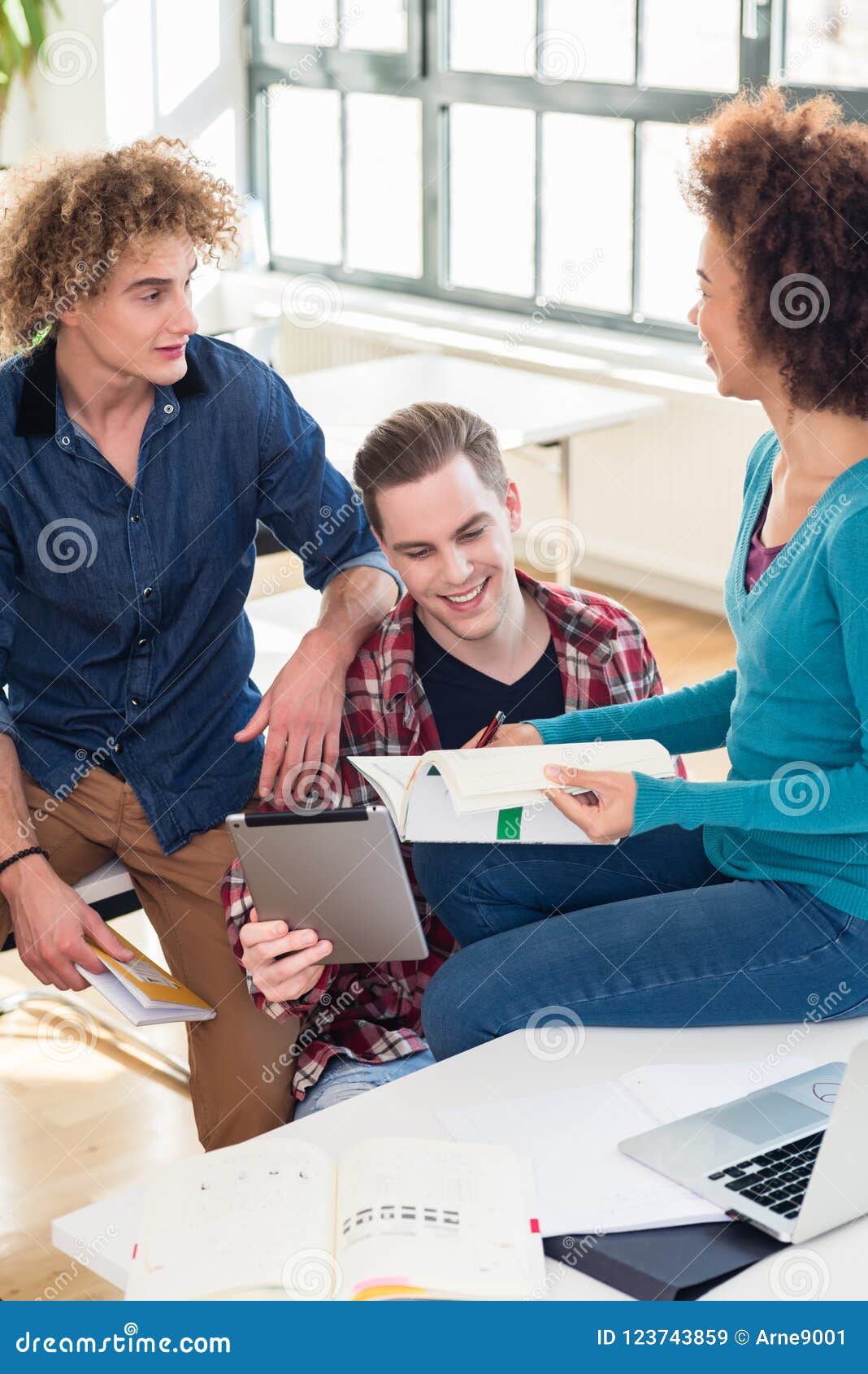 Three Young Students Using Both a Book and a Tablet PC for Checking ...