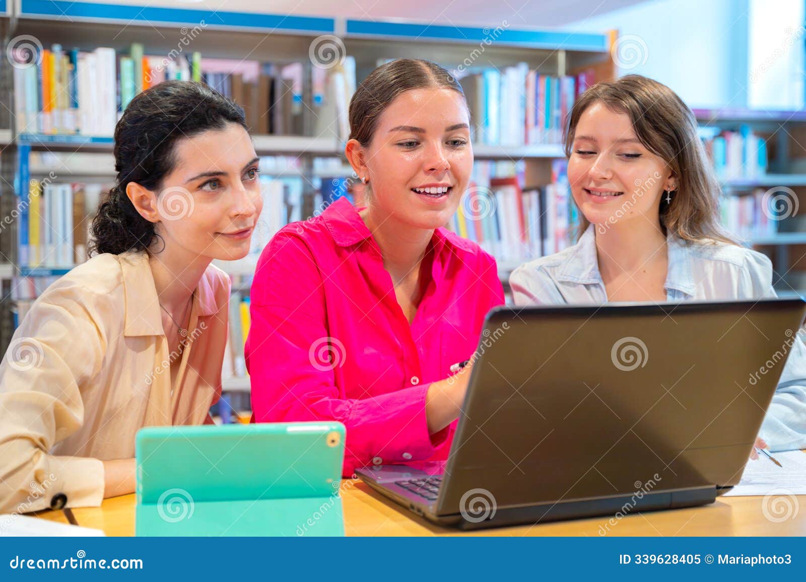Three Young Women Studying Together in a Library with Laptops and ...