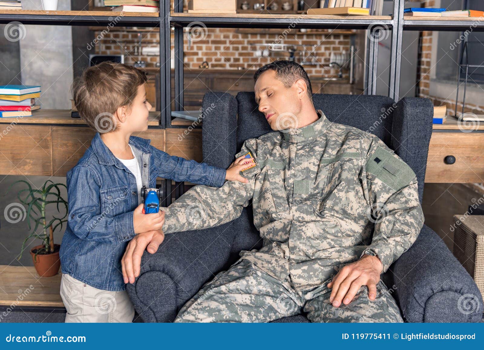 Tired Man In Military Uniform Sleeping On Armchair With Son Near Stock