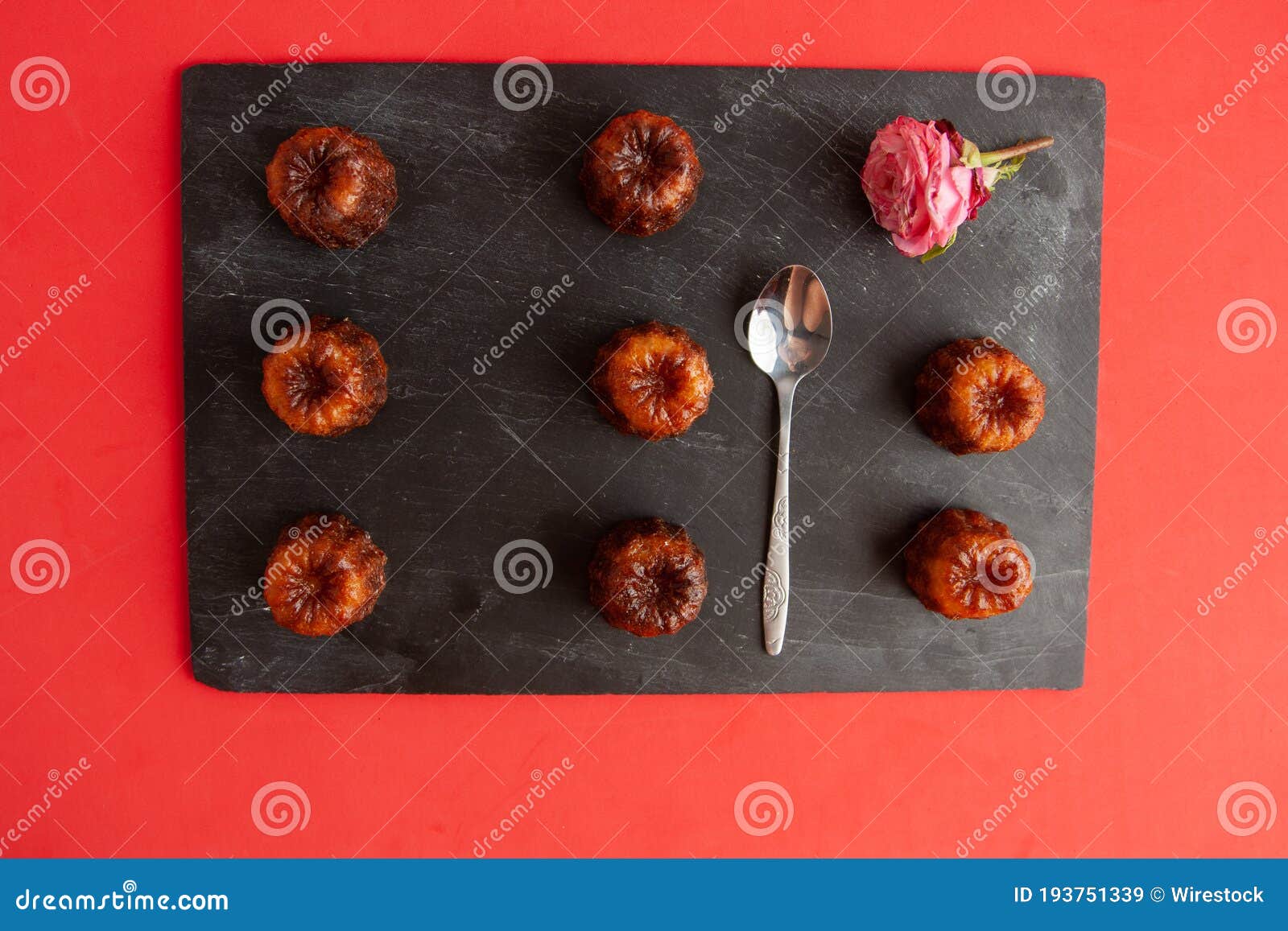 Top View of Caneles on a Tray with a Spoon and a Rose on a Red Surface ...