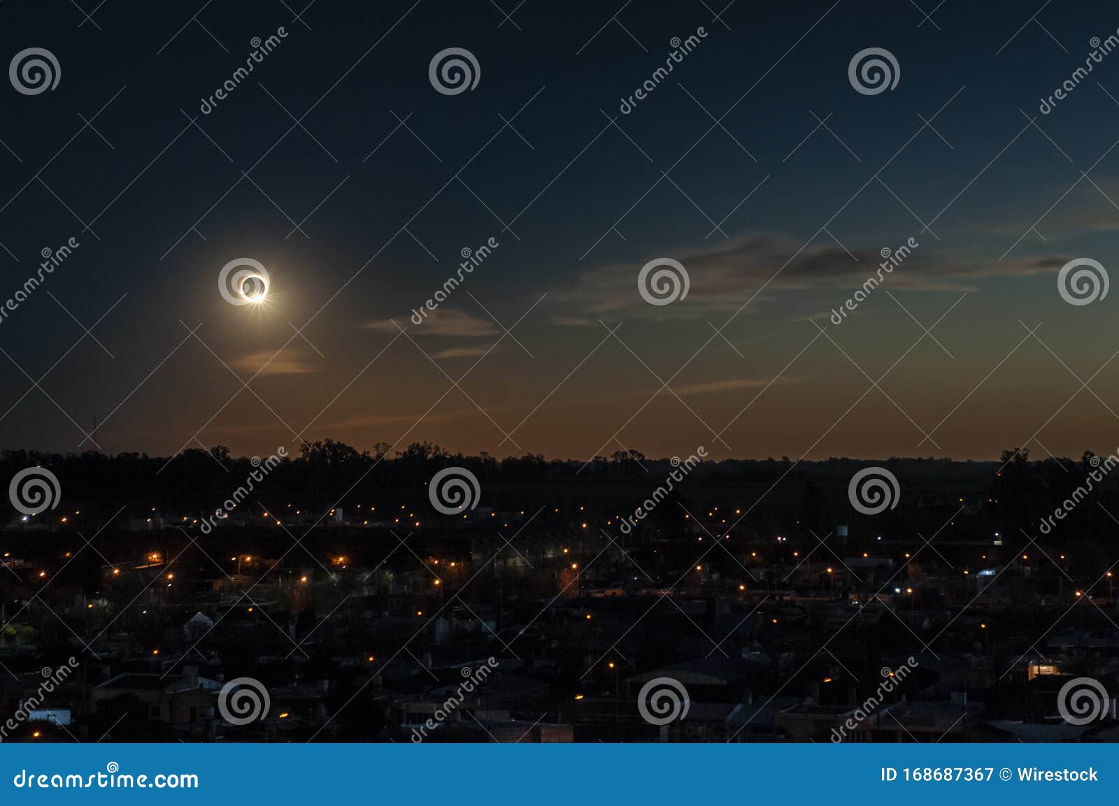 Total Solar Eclipse during the Evening Above a Town Surrounded by Trees ...